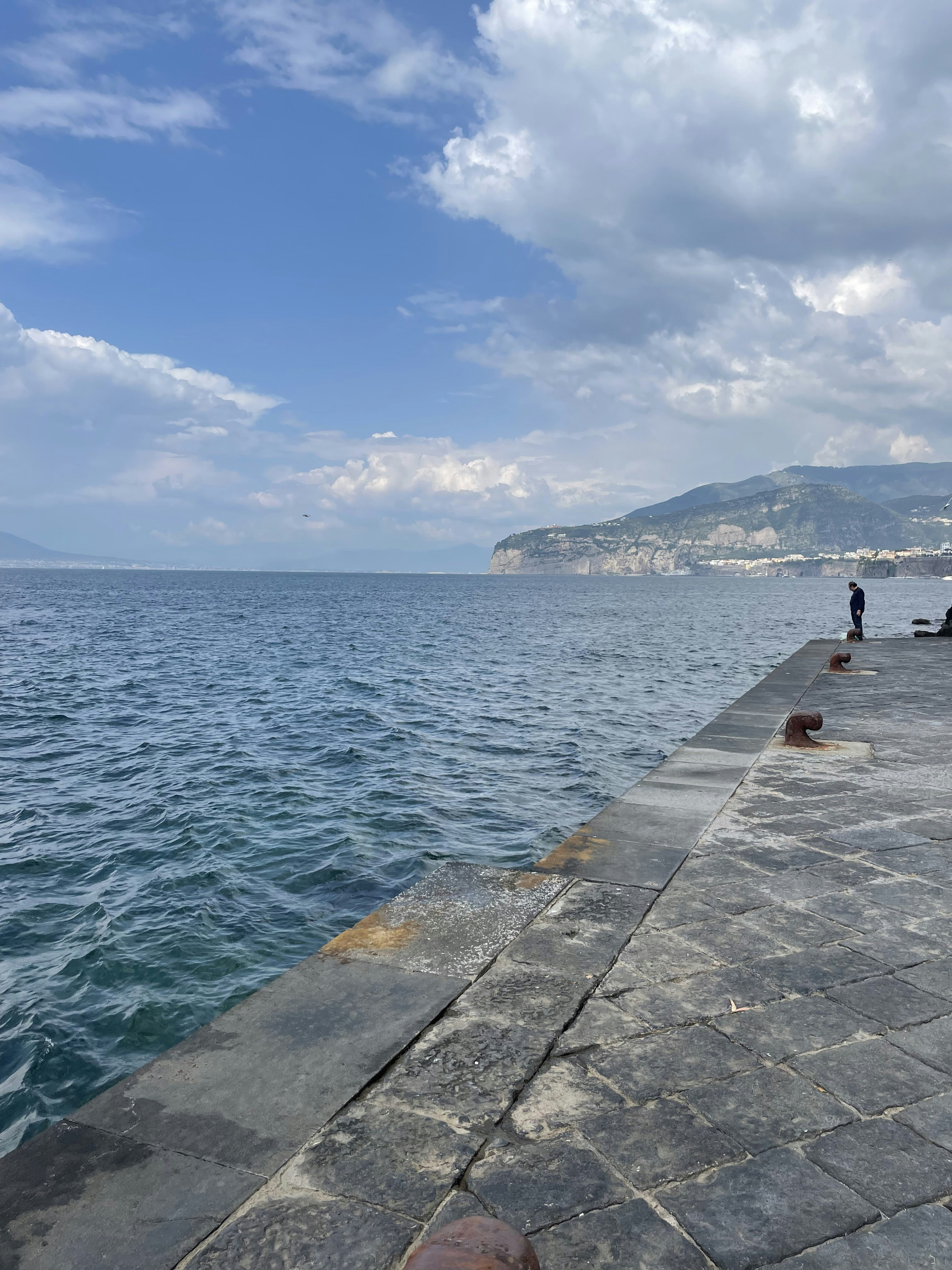 Edge of the Sea: A solitary figure on a weathered pier under a cloud-filled sky
