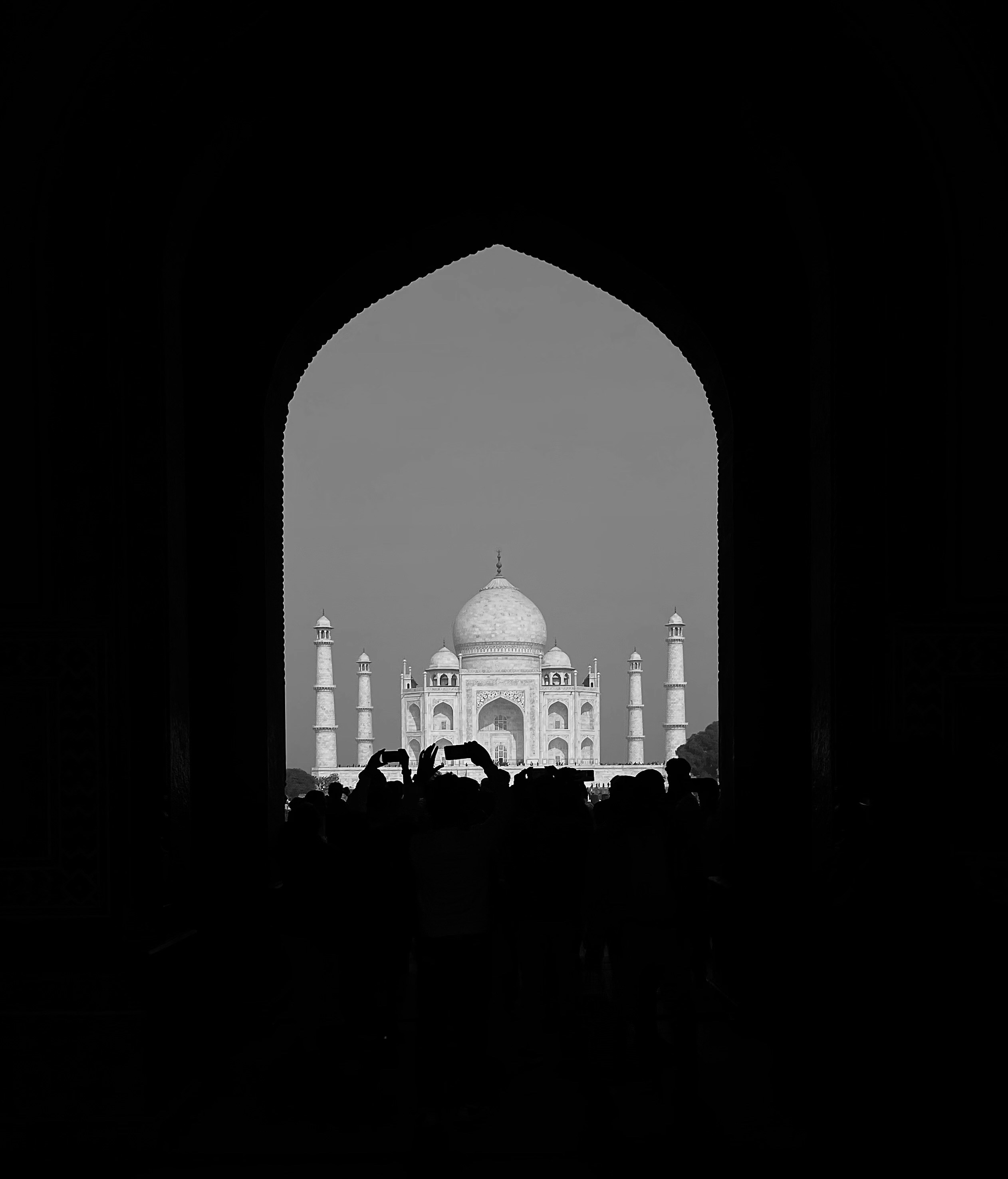 Silhouetted figures gather in an archway, framing the iconic Taj Mahal in the distance. The scene captures the interaction between visitors and this architectural marvel.