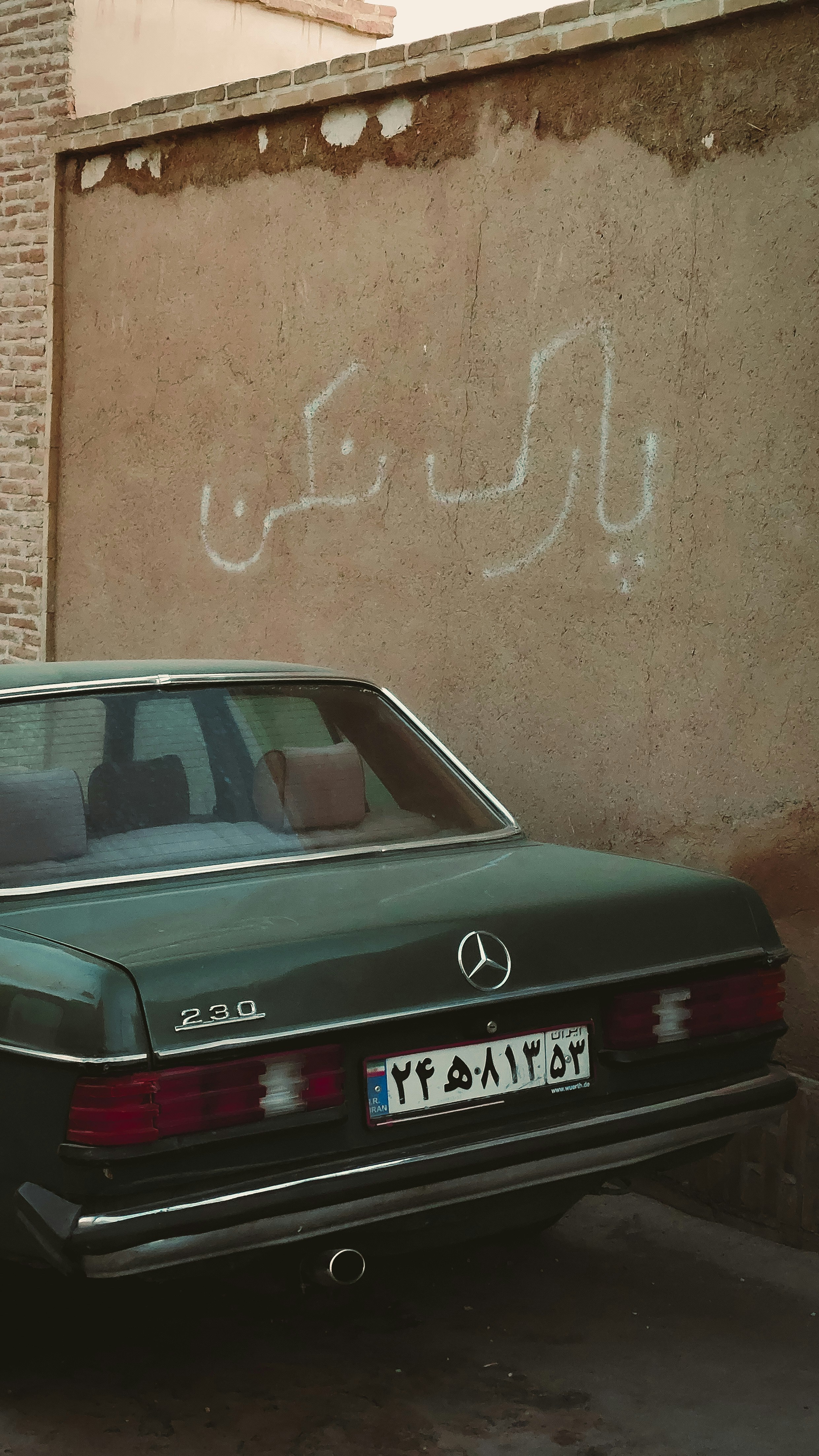 Photograph of a vintage green Mercedes 230 parked against a weathered wall with chalk graffiti.