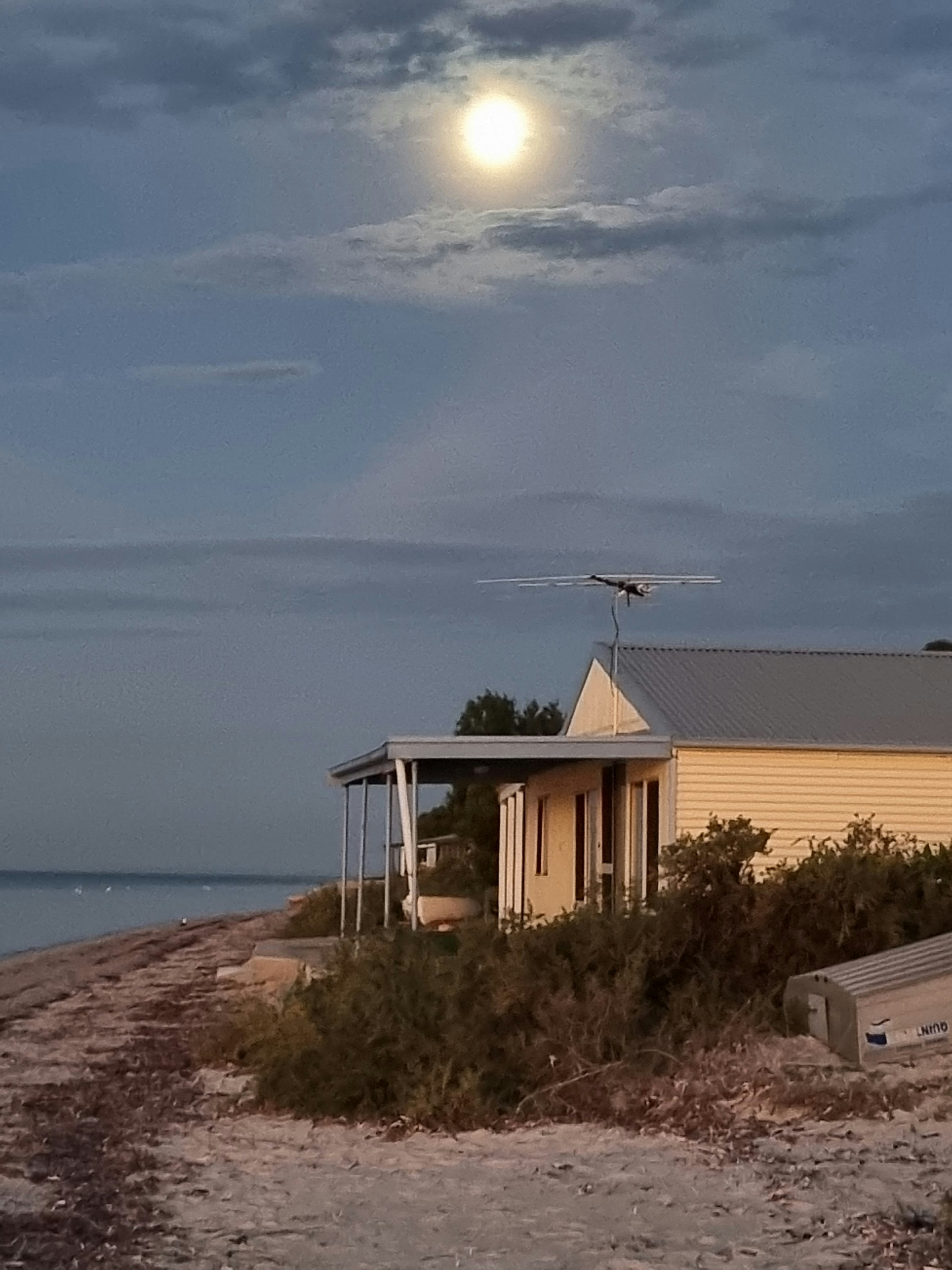 a house sitting on top of a sandy beach under a full moon