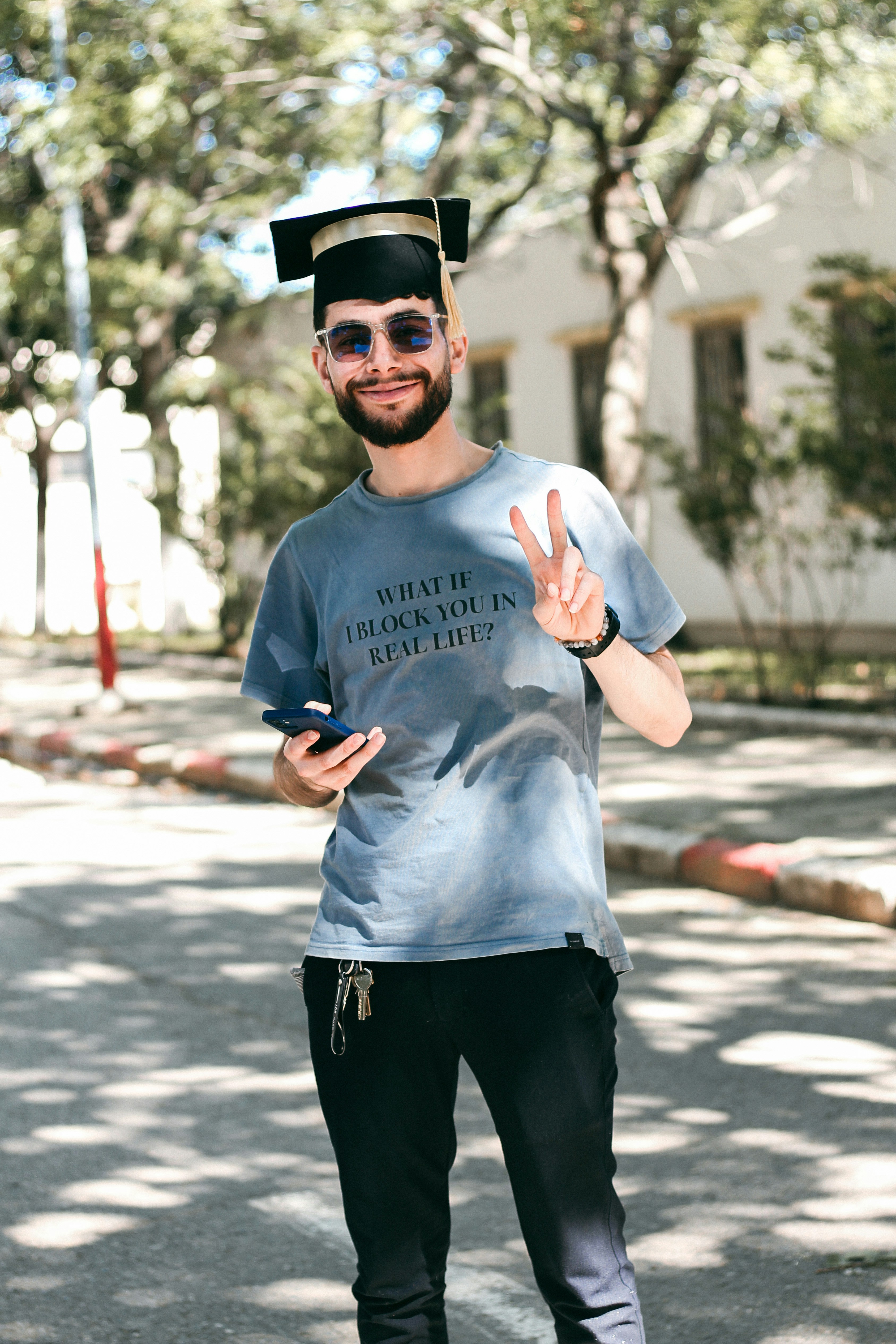 A man in a graduation cap and sunglasses giving the peace sign photo ...
