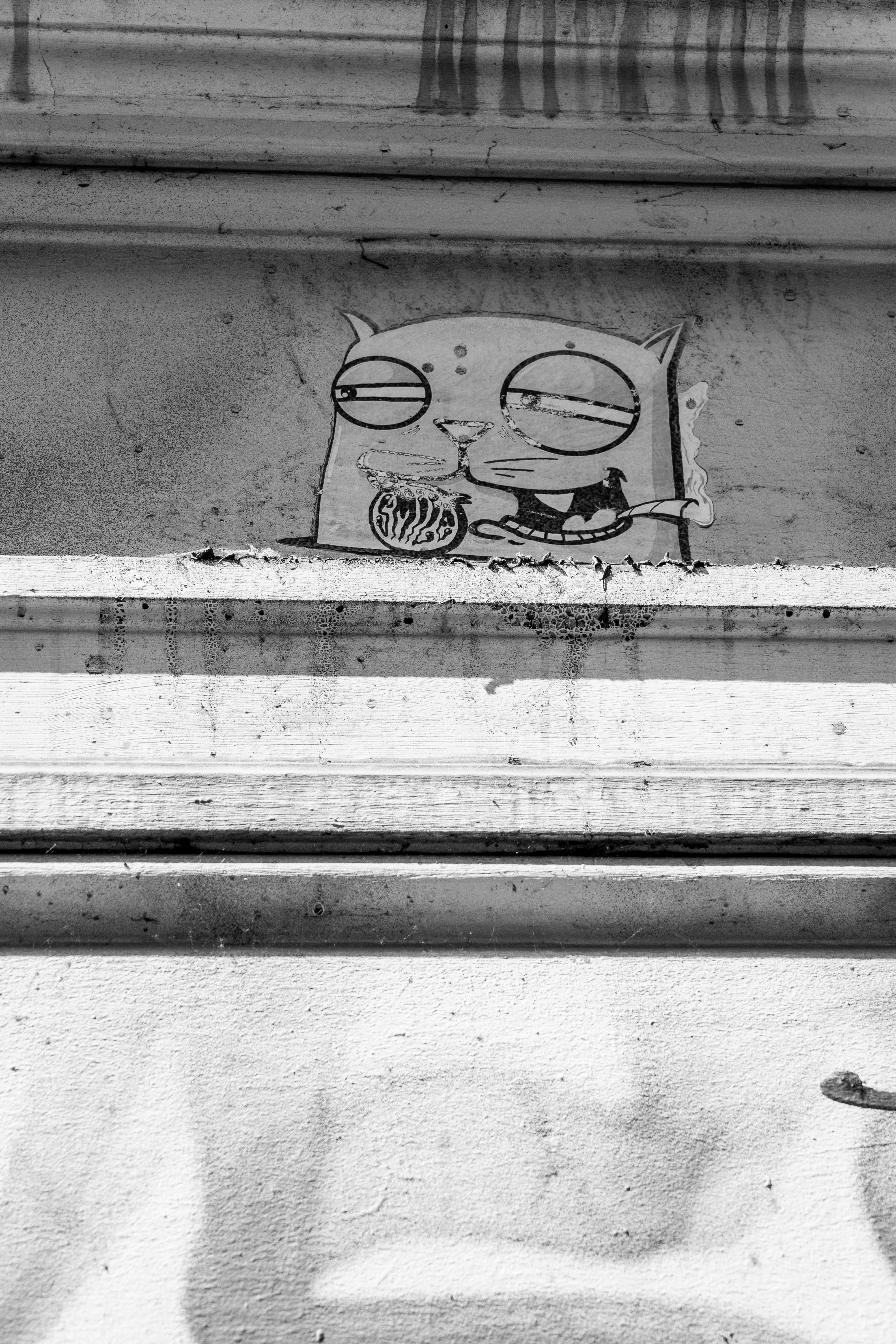 A quirky cartoon cat with a mischievous expression enjoying a snack, set against a weathered wall. The artwork adds character to the urban landscape.