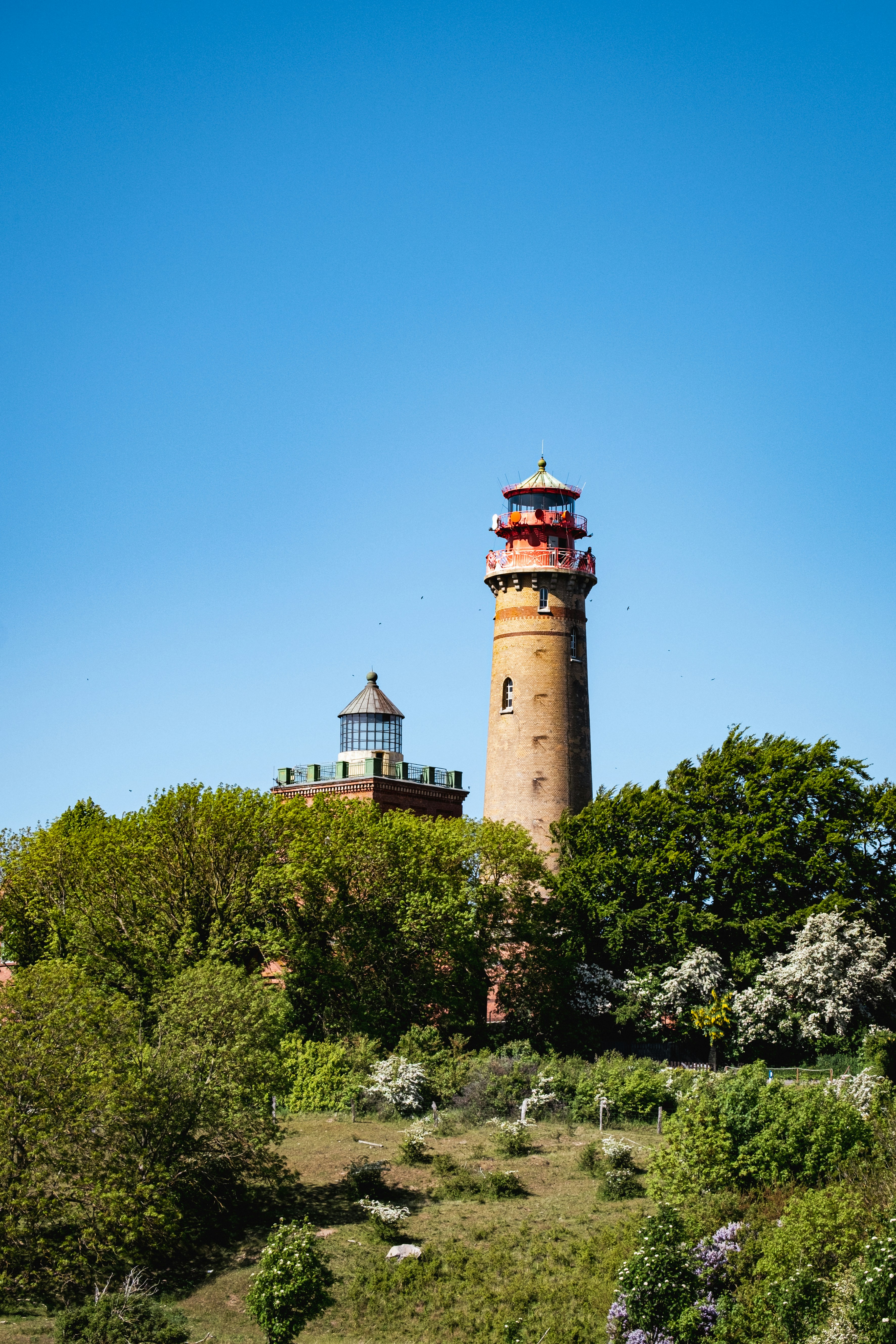 Beacon Above the Green: A Brick Lighthouse Reaching Toward a Clear Blue Sky