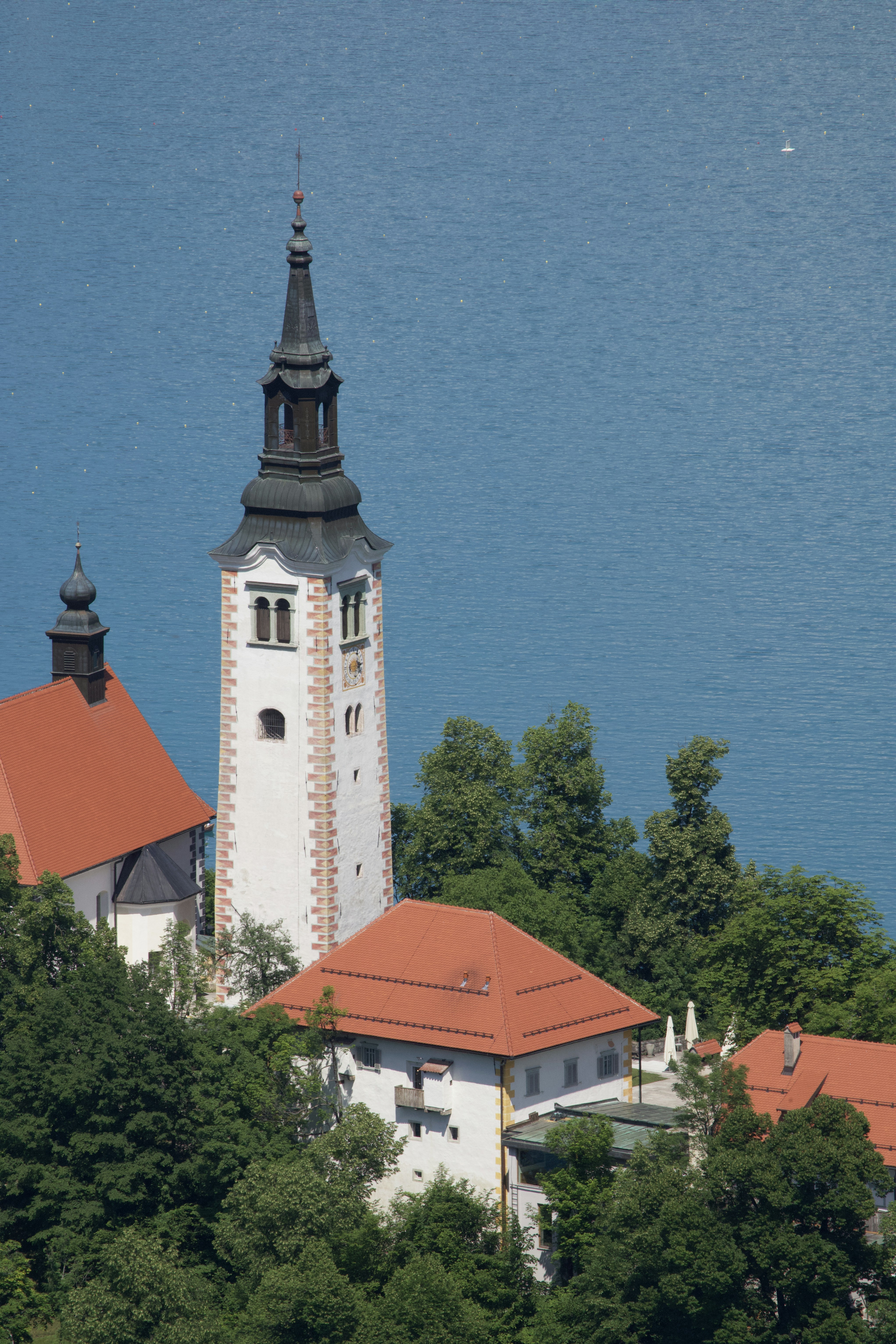 Lakeside Bell-Tower Emerges Above Red Roofs and Green Foliage