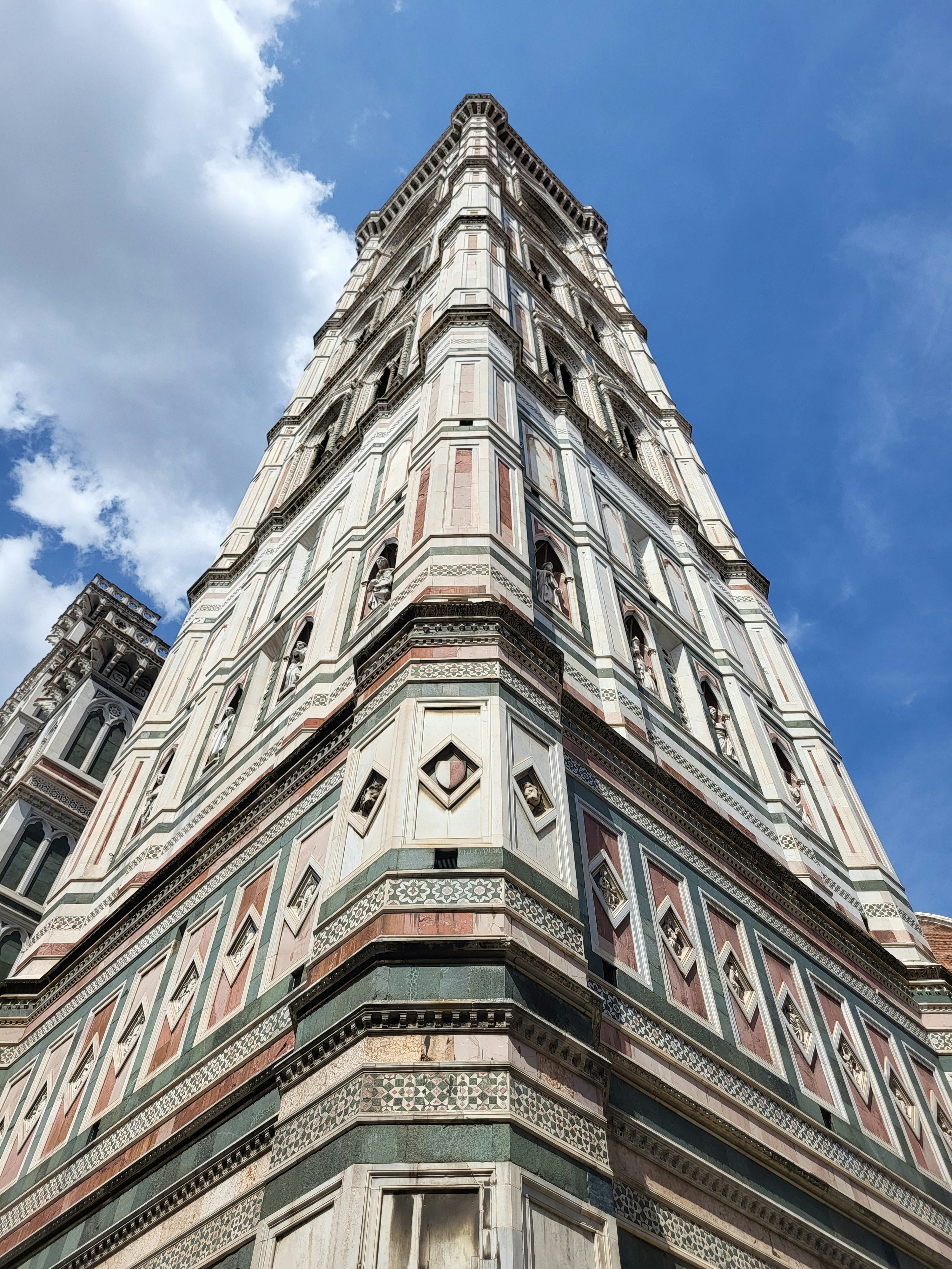 Tall, intricately tiled corner tower rises at a sharp angle against a blue sky, featuring geometric patterns and arched openings.