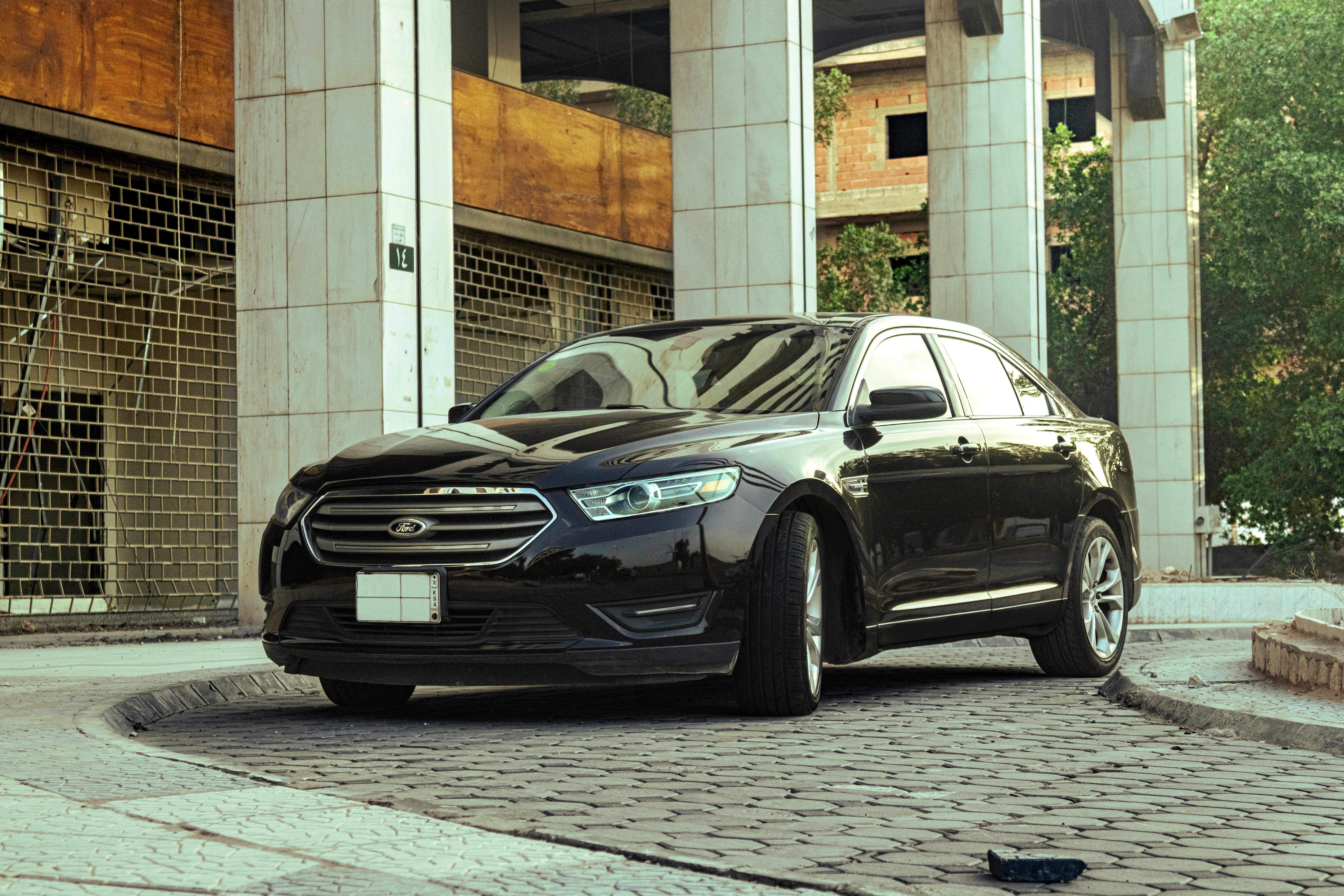 Sleek black sedan parked in a modern urban setting, surrounded by tall concrete columns and greenery.