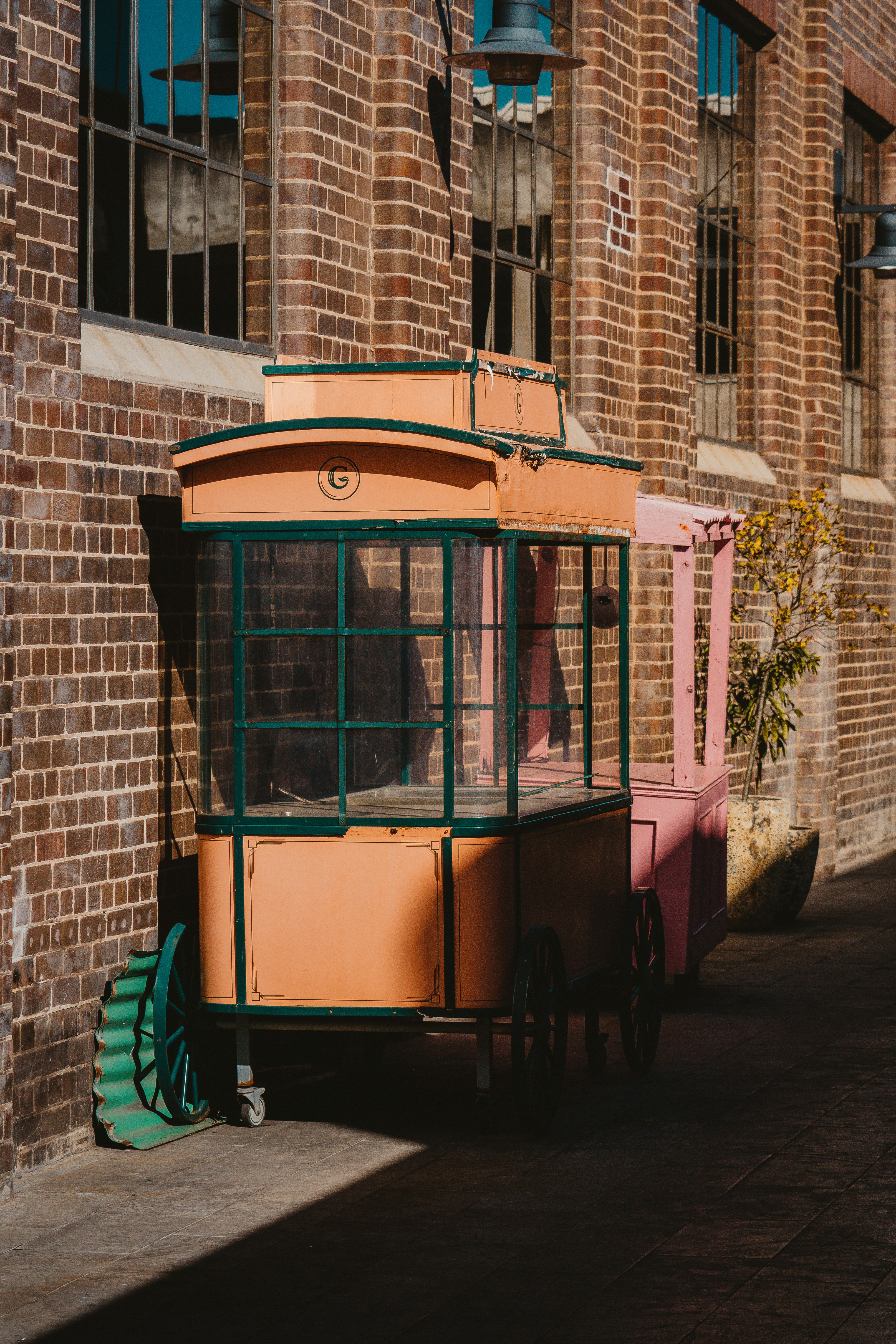 Sunlit Peach Kiosk with Teal Windows Along a Brick-Walled Street