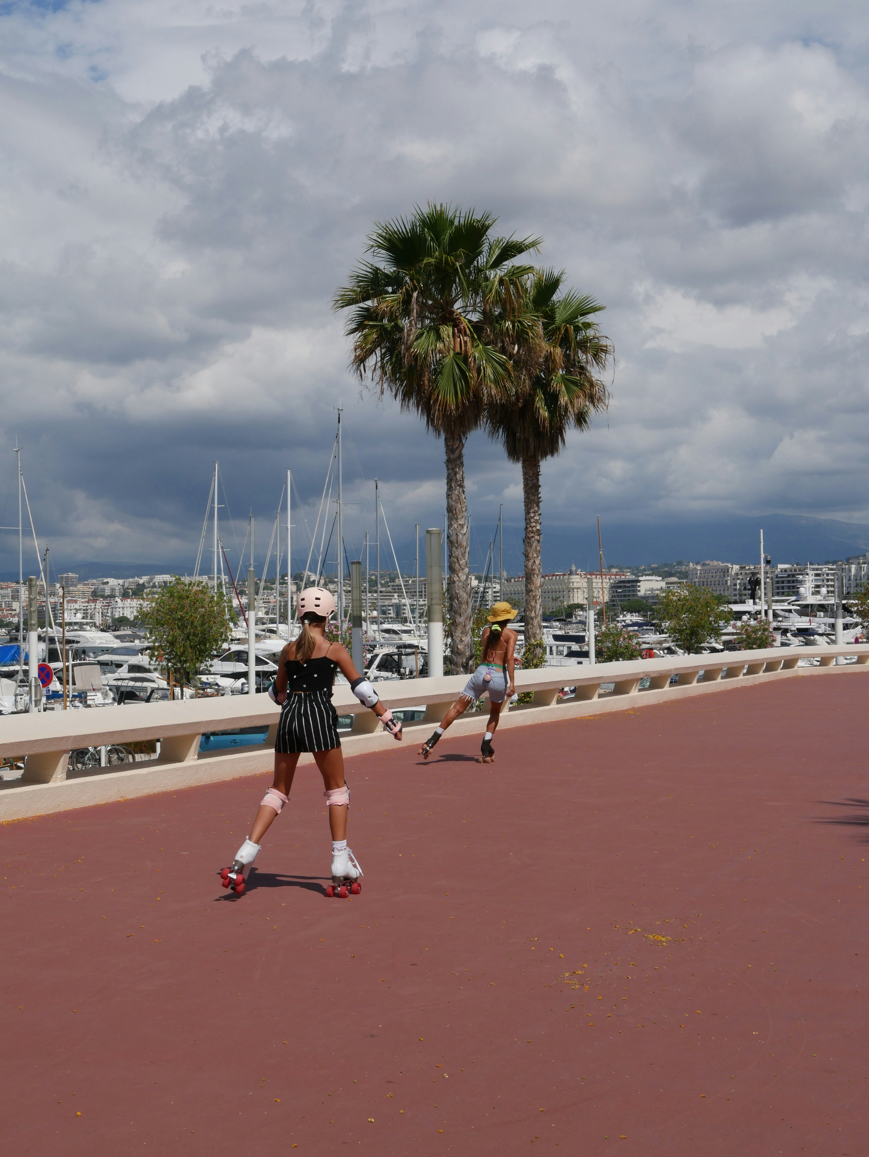 Two Skaters Glide Along a Palm-Tree Marina Promenade Under Cloudy Skies