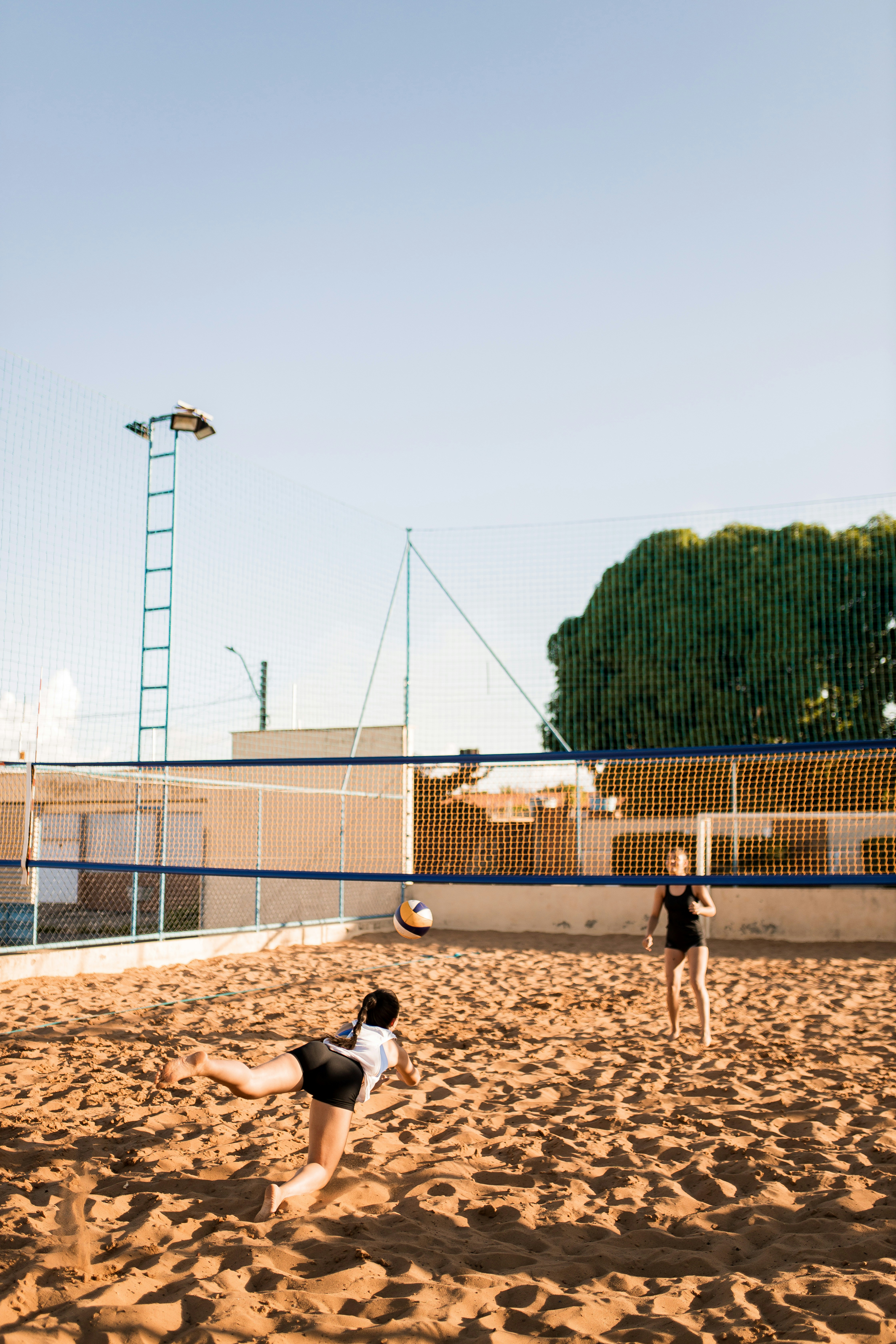 Airborne dig over sunlit sand on an urban beach volleyball court