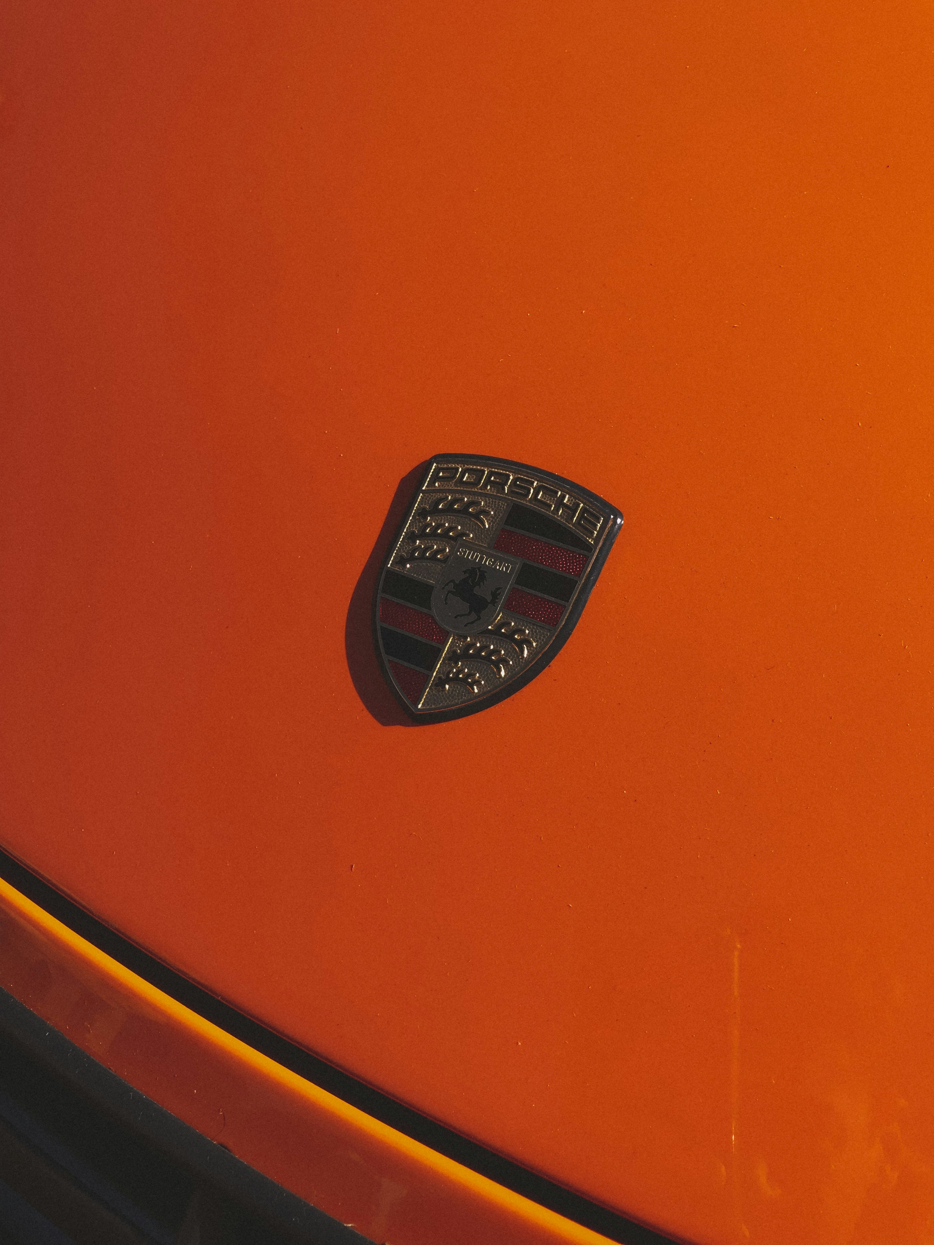 Close-up of a Porsche logo on an orange car hood under soft lighting.
