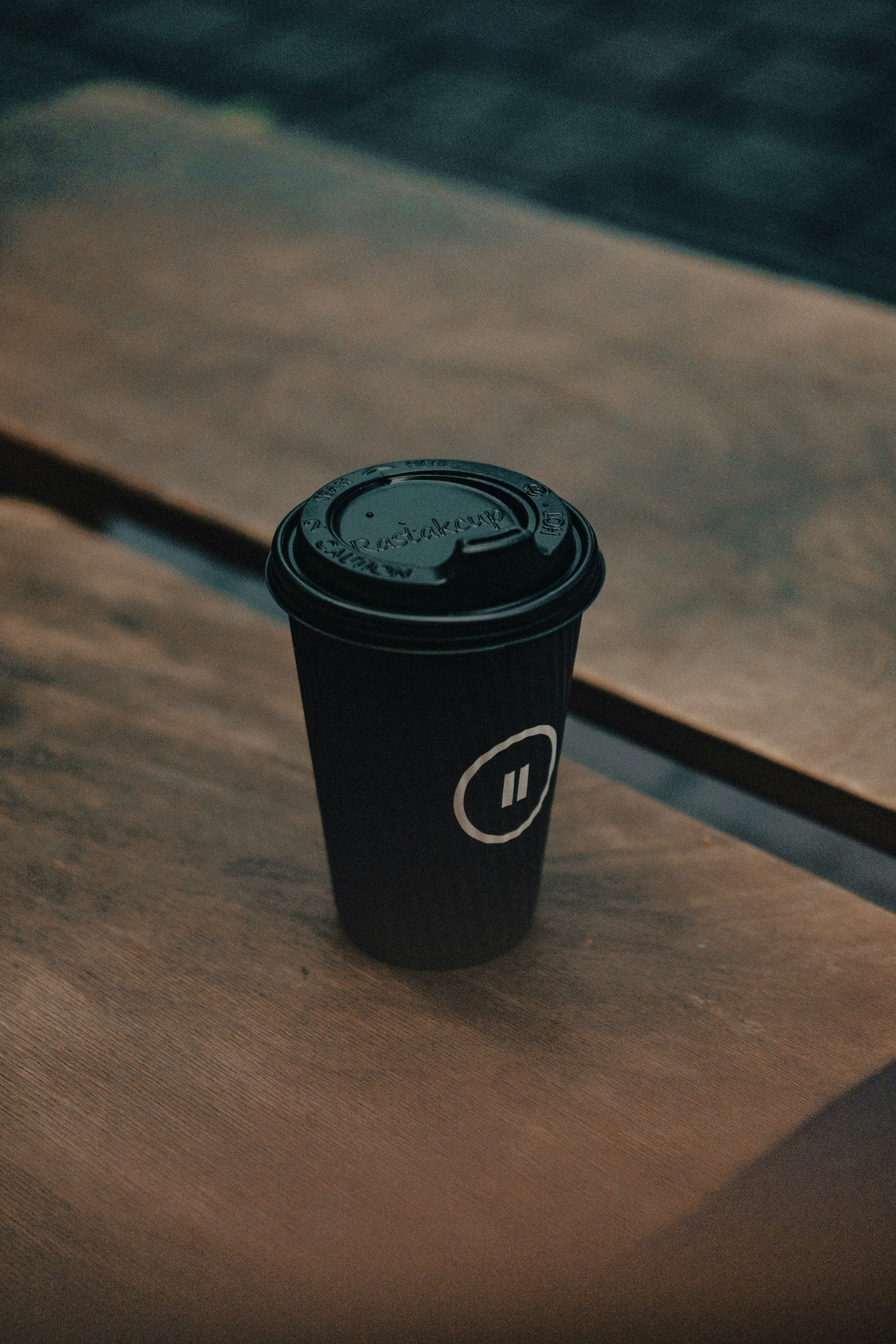 Dockside Quiet: A Black To-Go Cup Perched on Weathered Planks by the Water