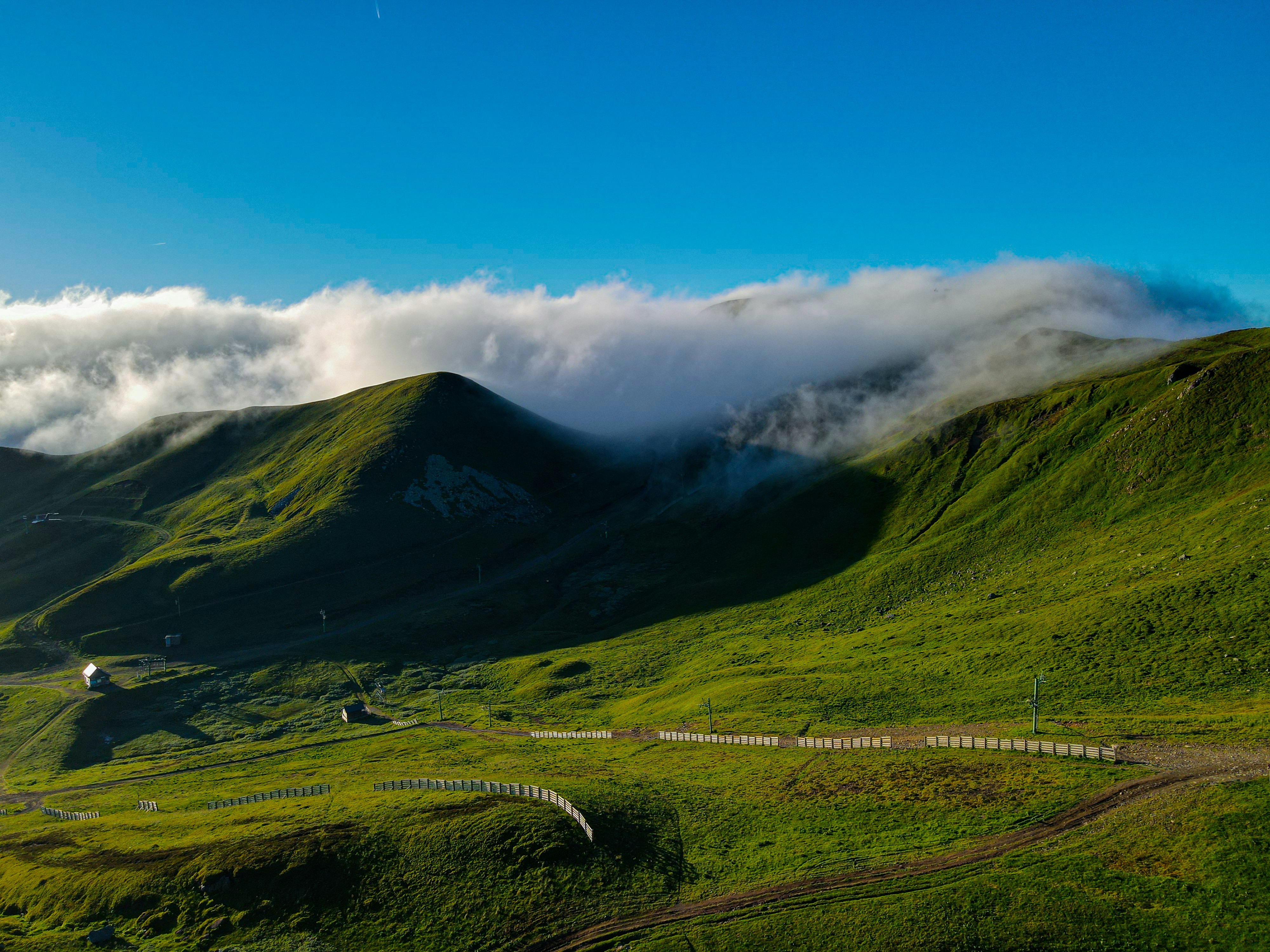 Lush green hills with winding paths under a canopy of low-hanging clouds.