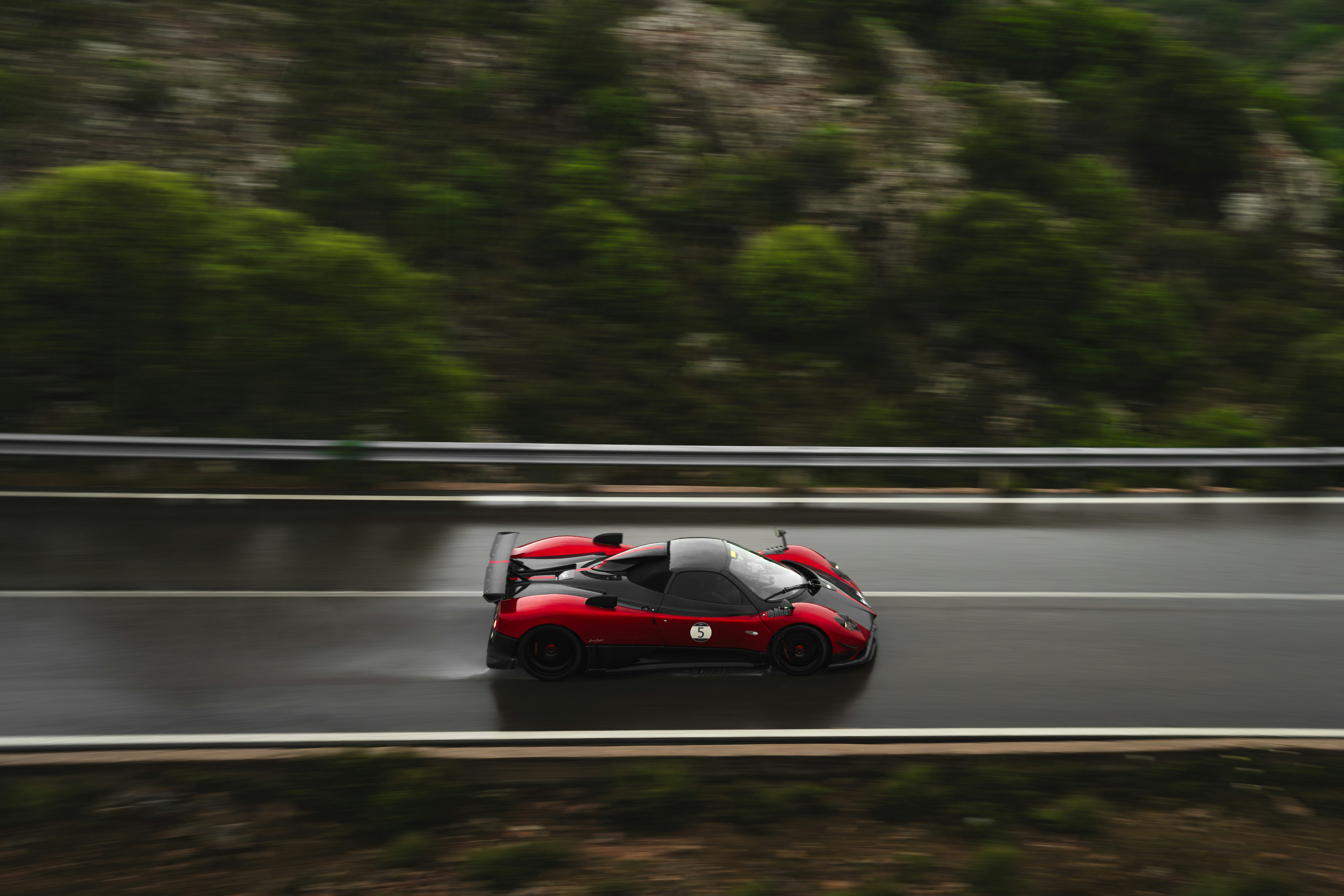 A sleek red sports car glides along a rain-soaked road, showcasing its aerodynamic design and dynamic motion.