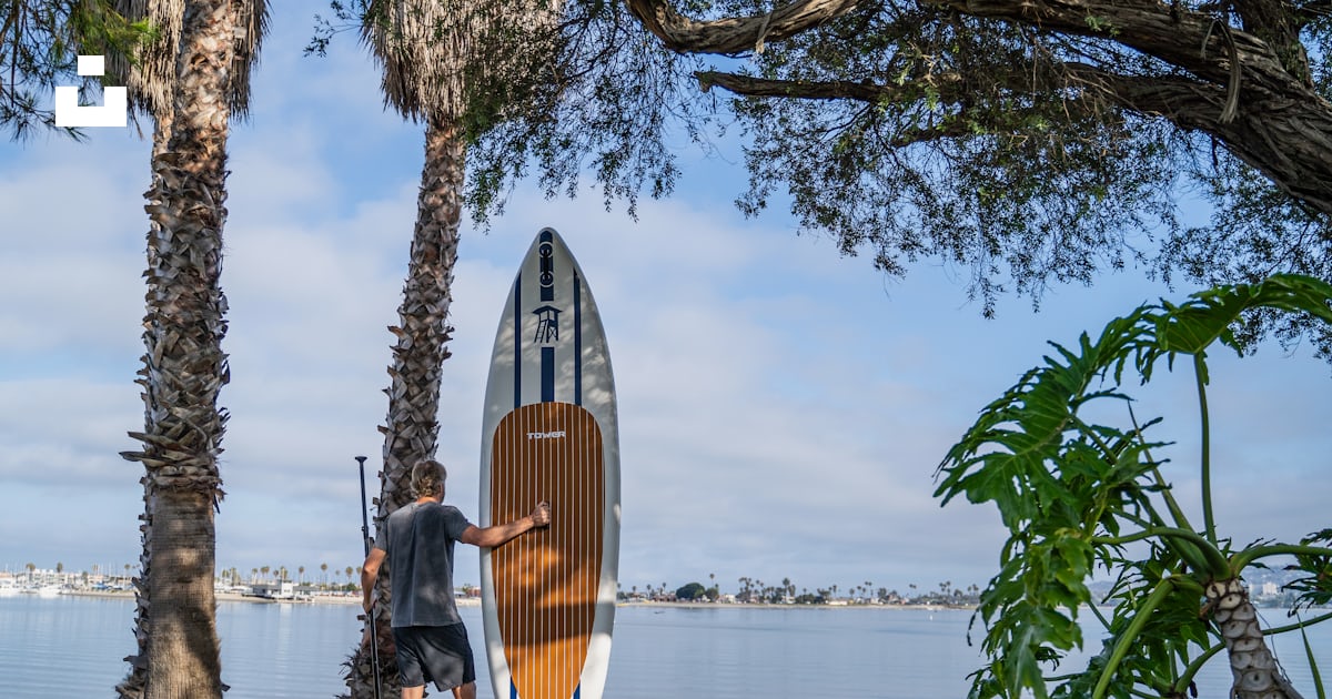 Un Homme Debout à Côté Dune Planche De Surf Sur Un Champ Verdoyant