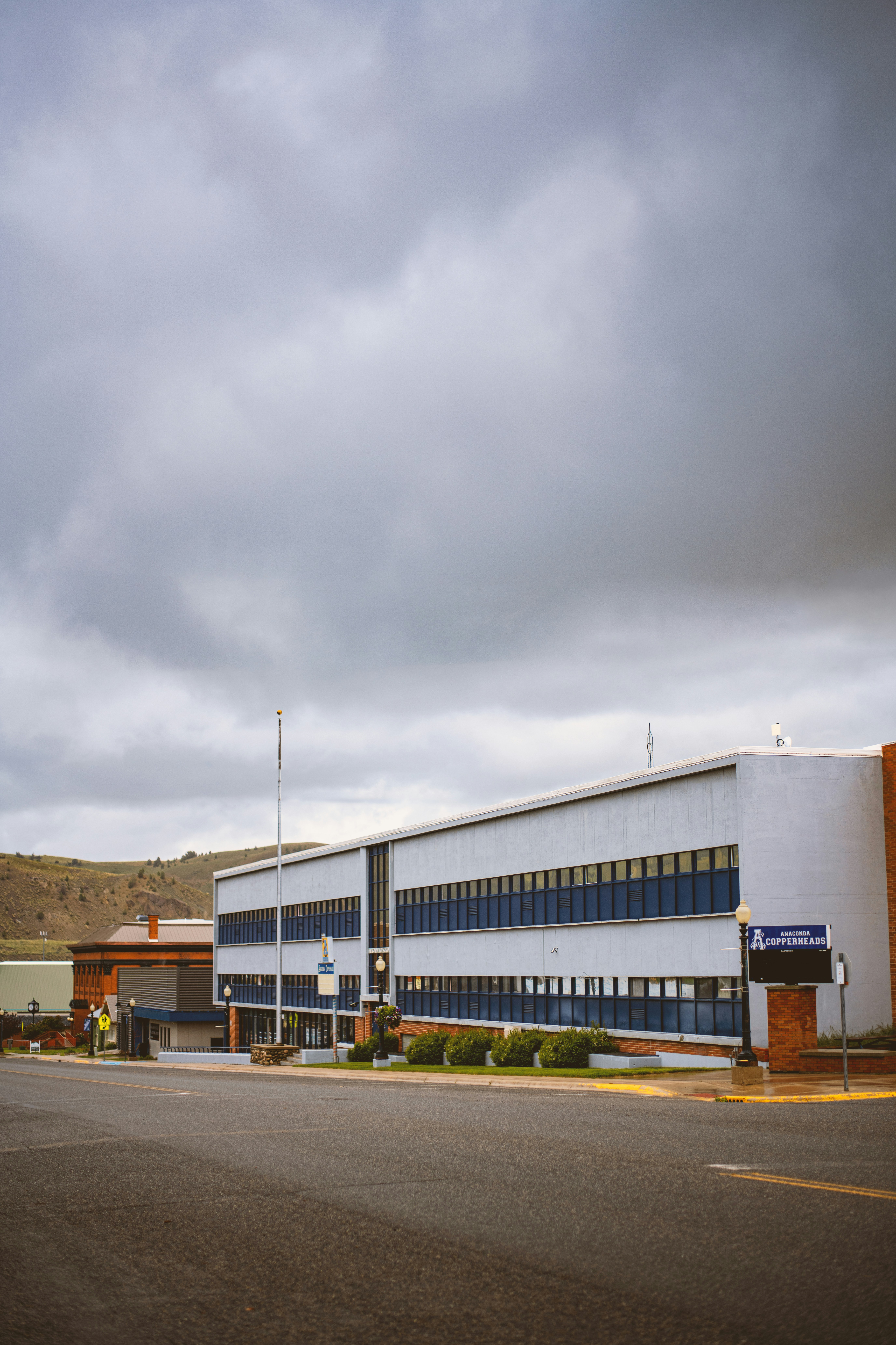 A contemporary building with large windows and a prominent sign stands along a quiet street, framed by overcast skies. The scene captures a blend of urban design and natural elements.