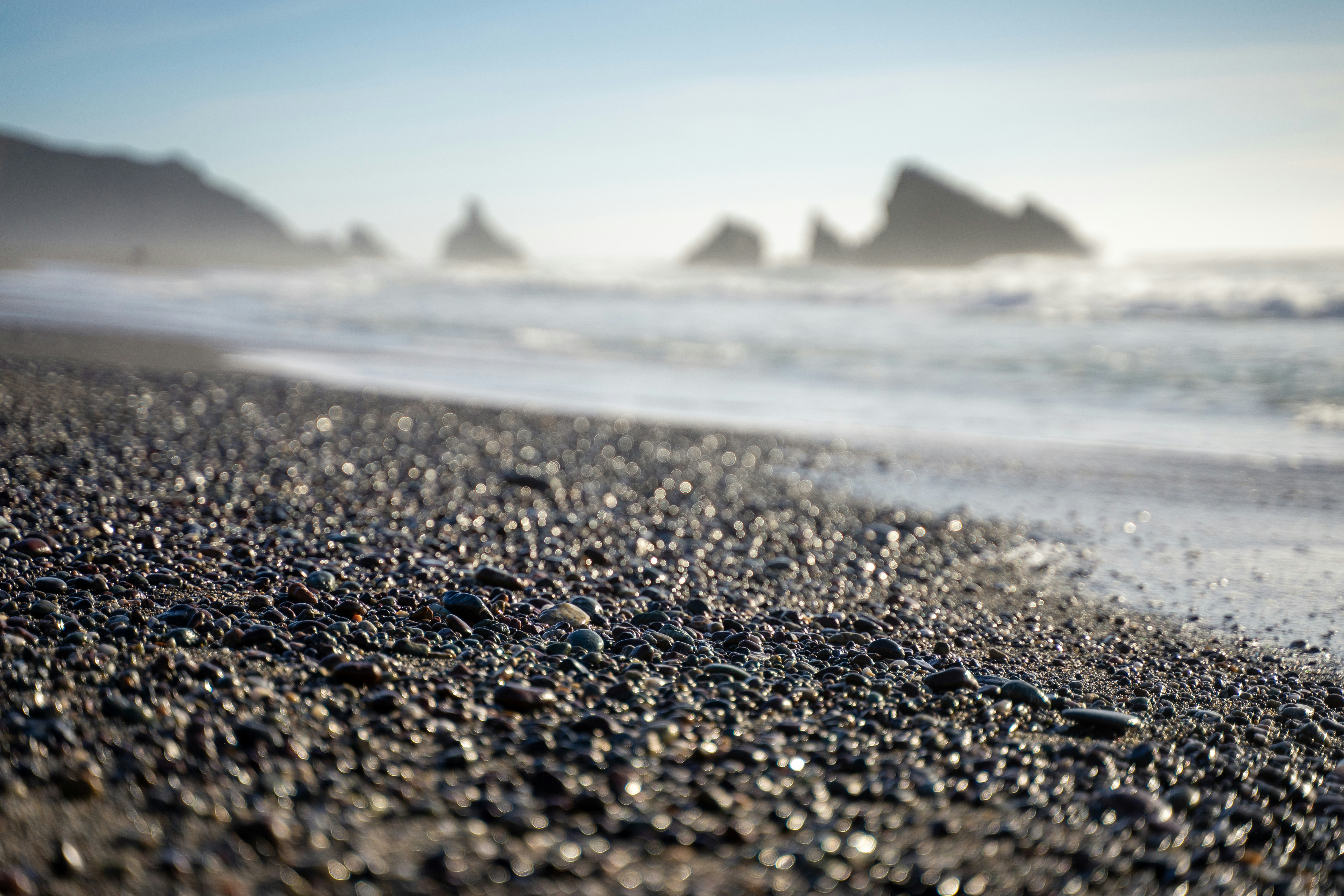 Glistening Pebbles at the Quiet Shoreline with Distant Sea-Rock Silhouettes