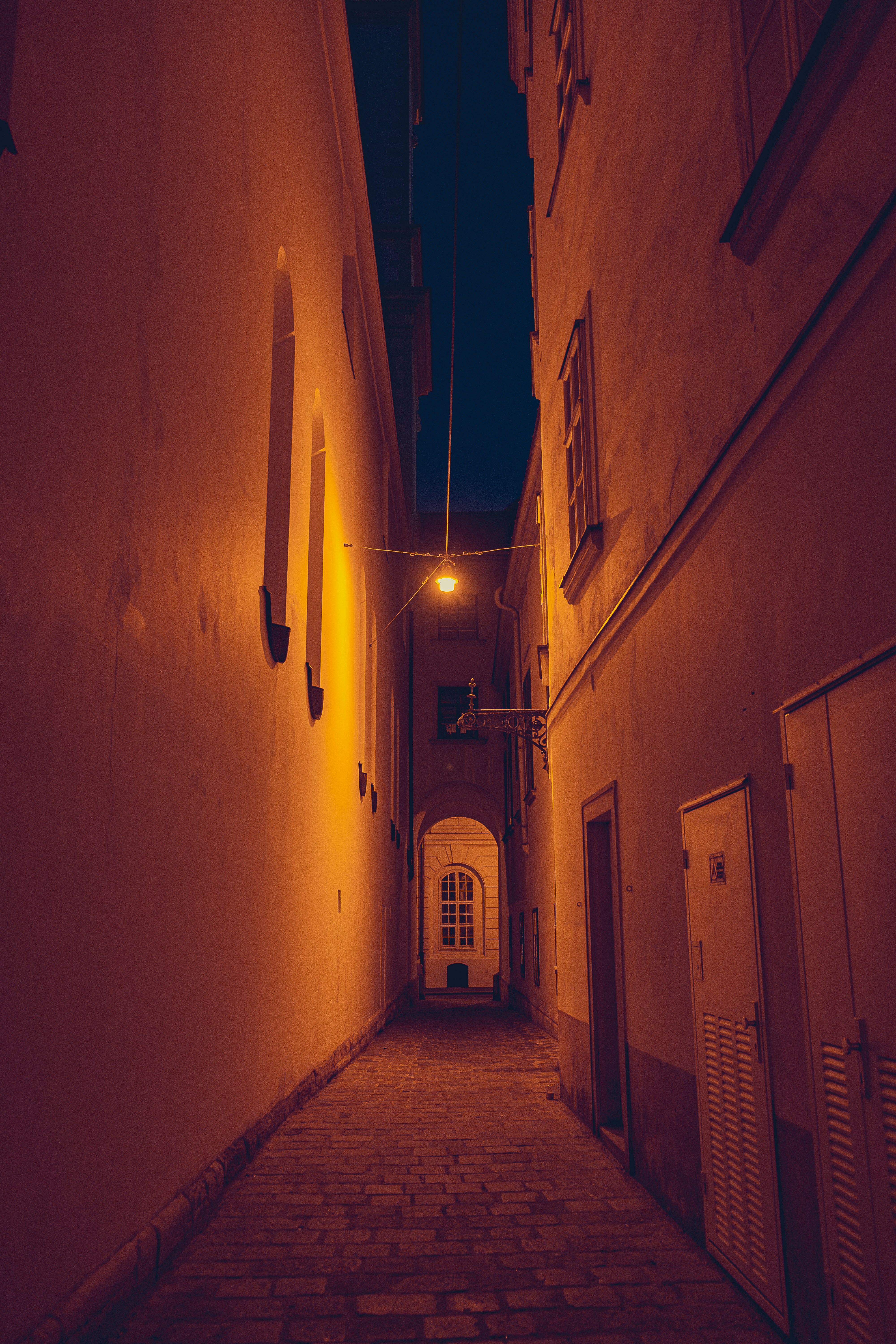 Dimly lit alleyway with warm orange tones leading to an archway, evoking a sense of mystery and solitude.
