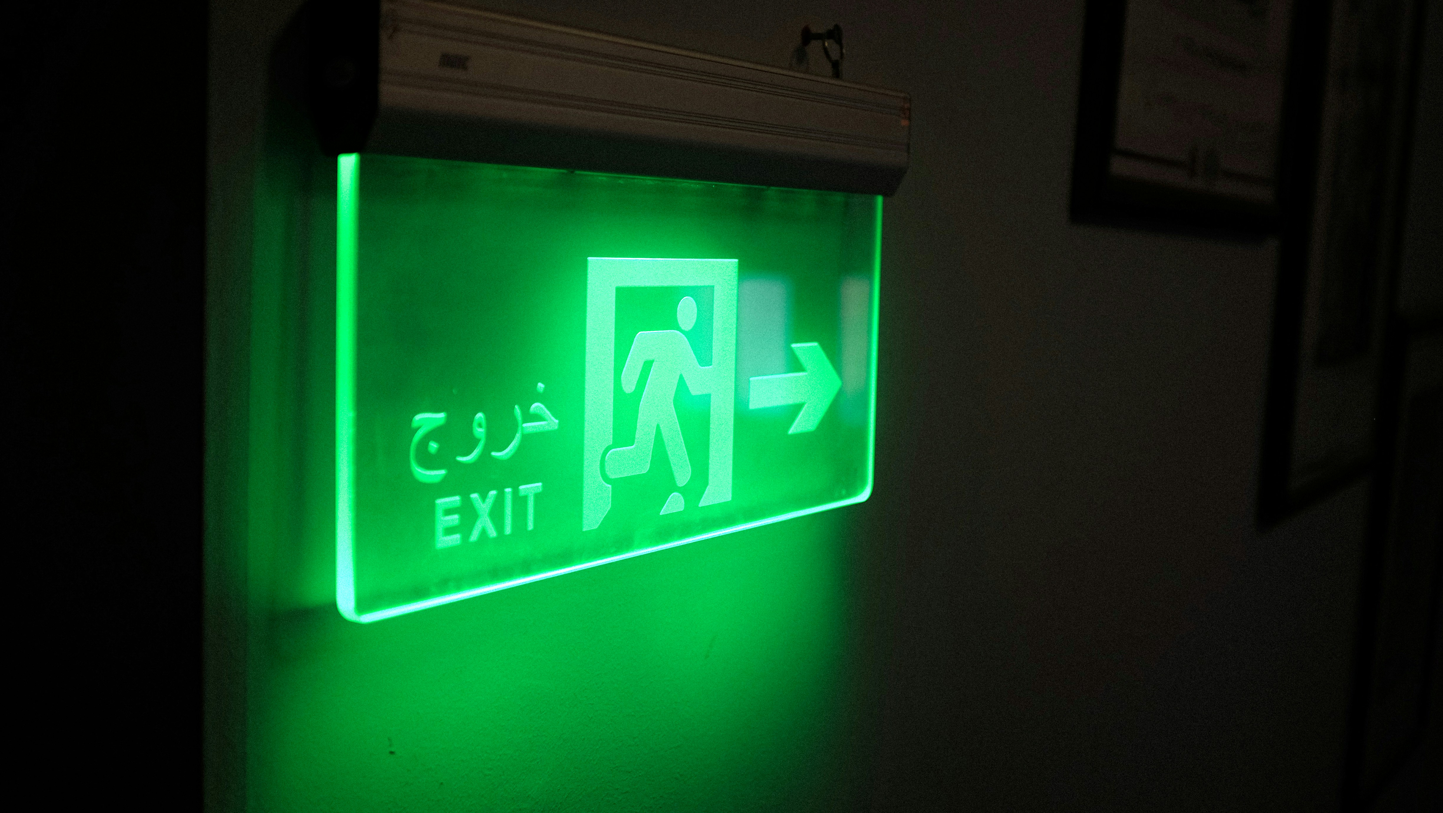 Green Exit in Darkness: Neon Safety Sign Illuminates the Hall
