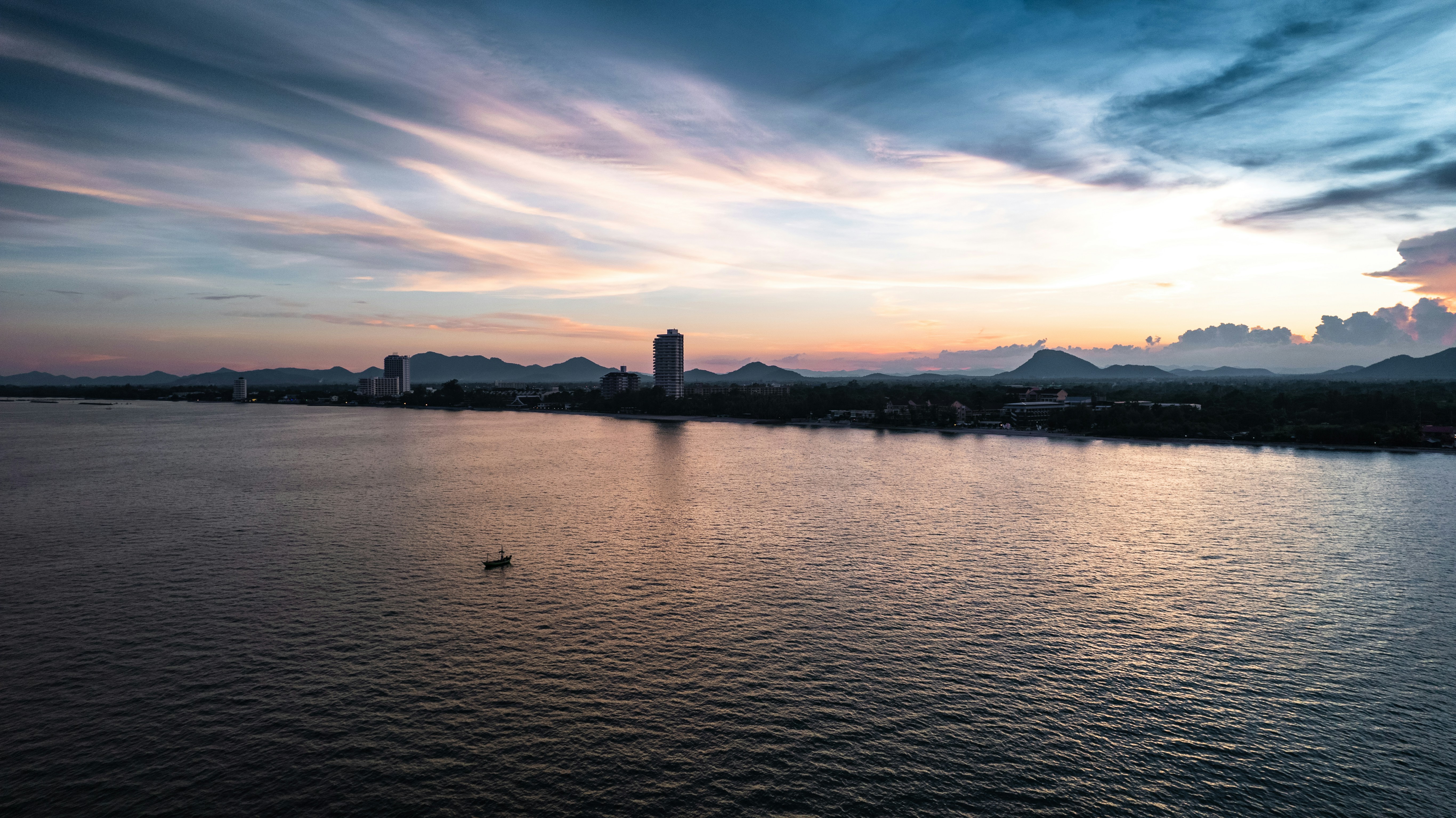 Calm sea reflecting the colorful sky at dusk near a distant city skyline.