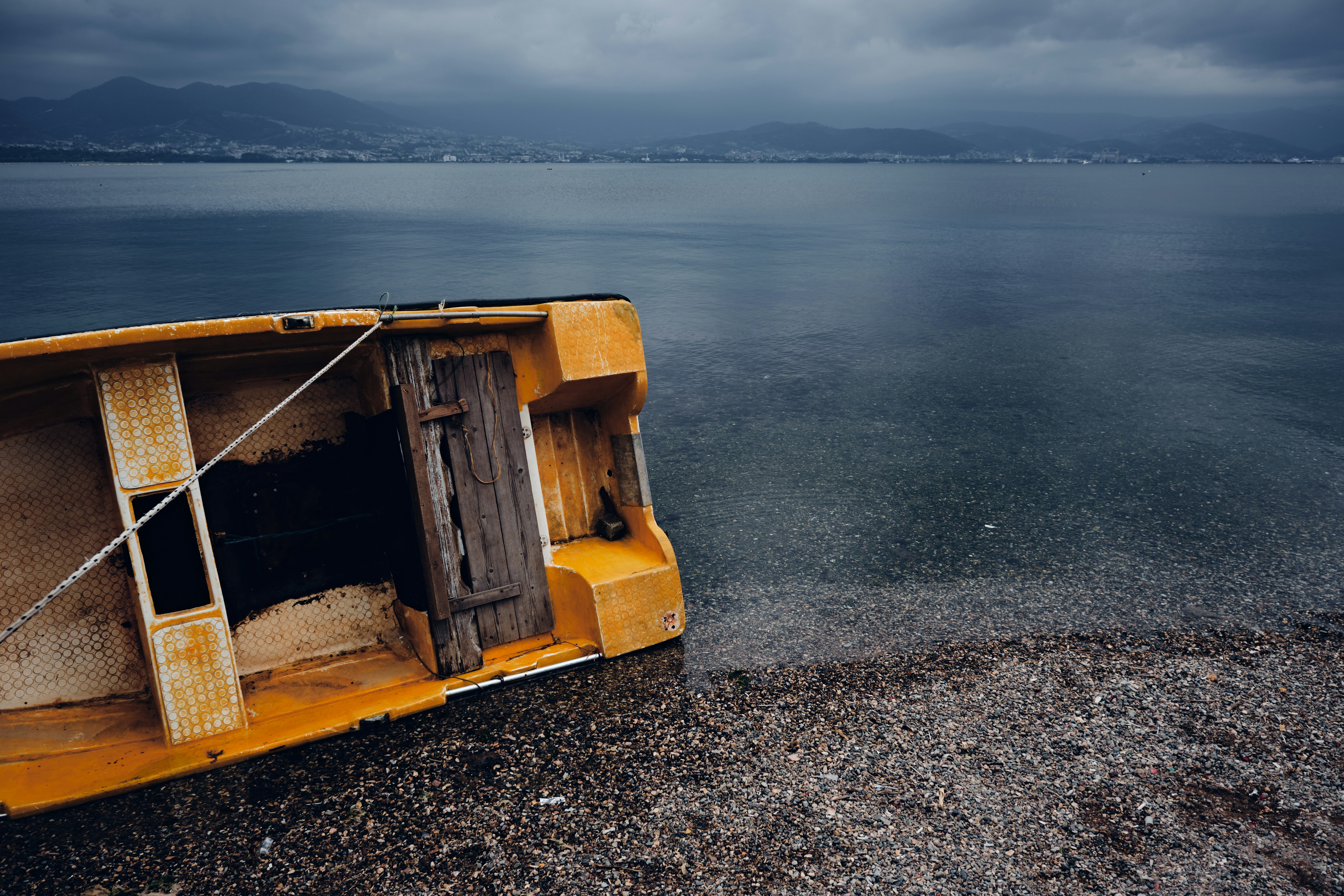 Rust and Pebbles: A Weathered Yellow Hull by the Quiet Sea
