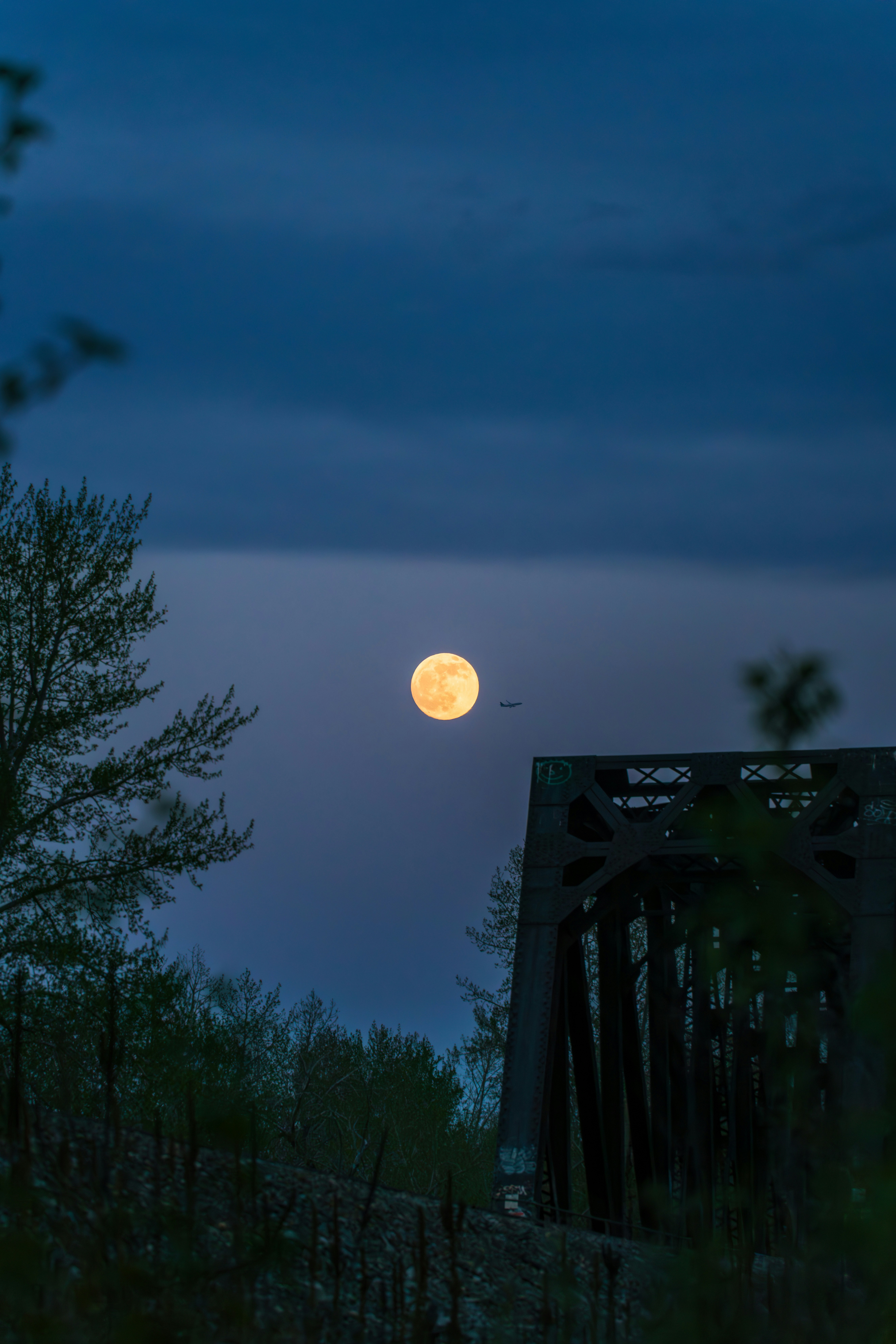 Moonrise over a solitary steel truss bridge at blue hour