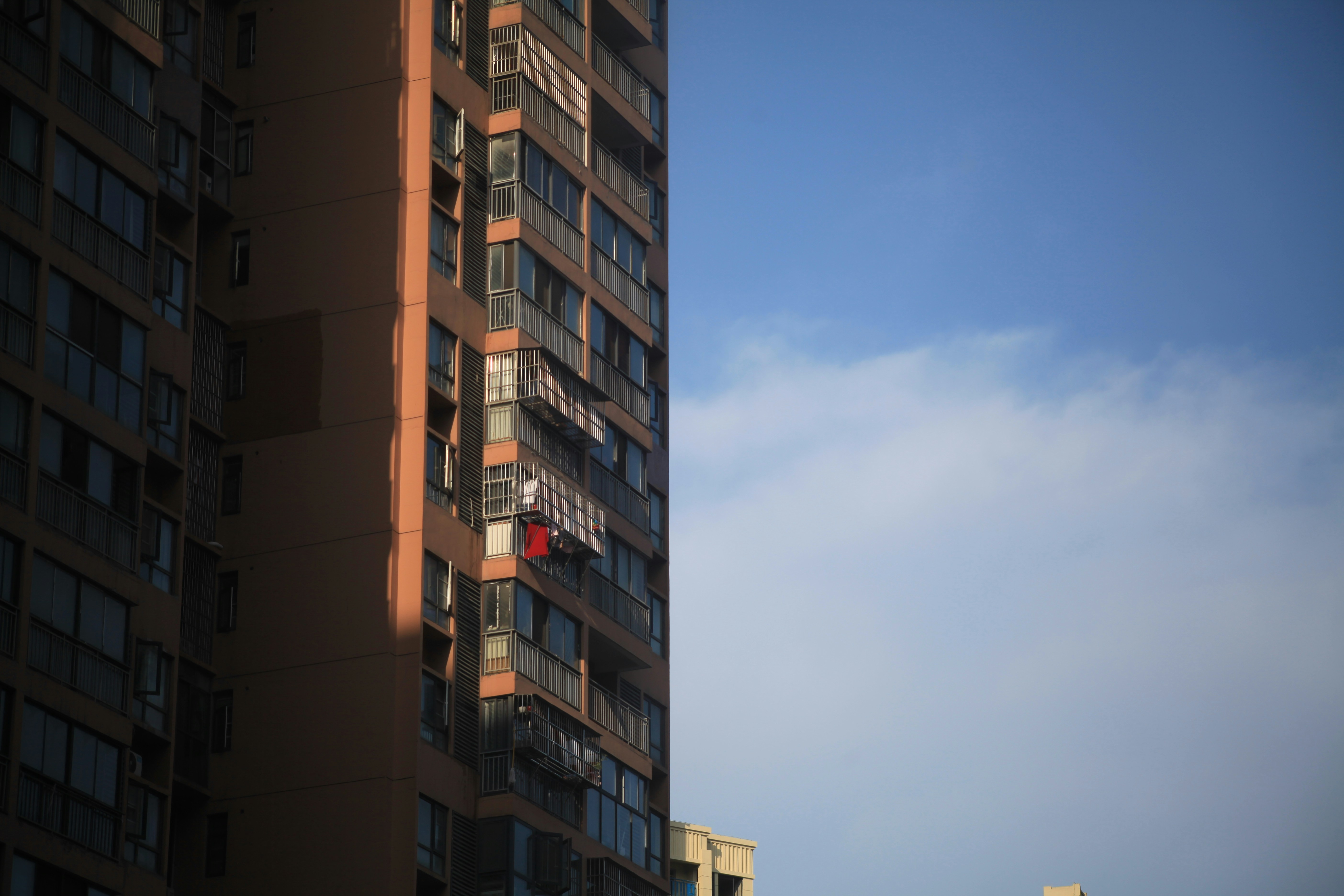 Crimson Figure on a Balcony Against a Clear City Sky