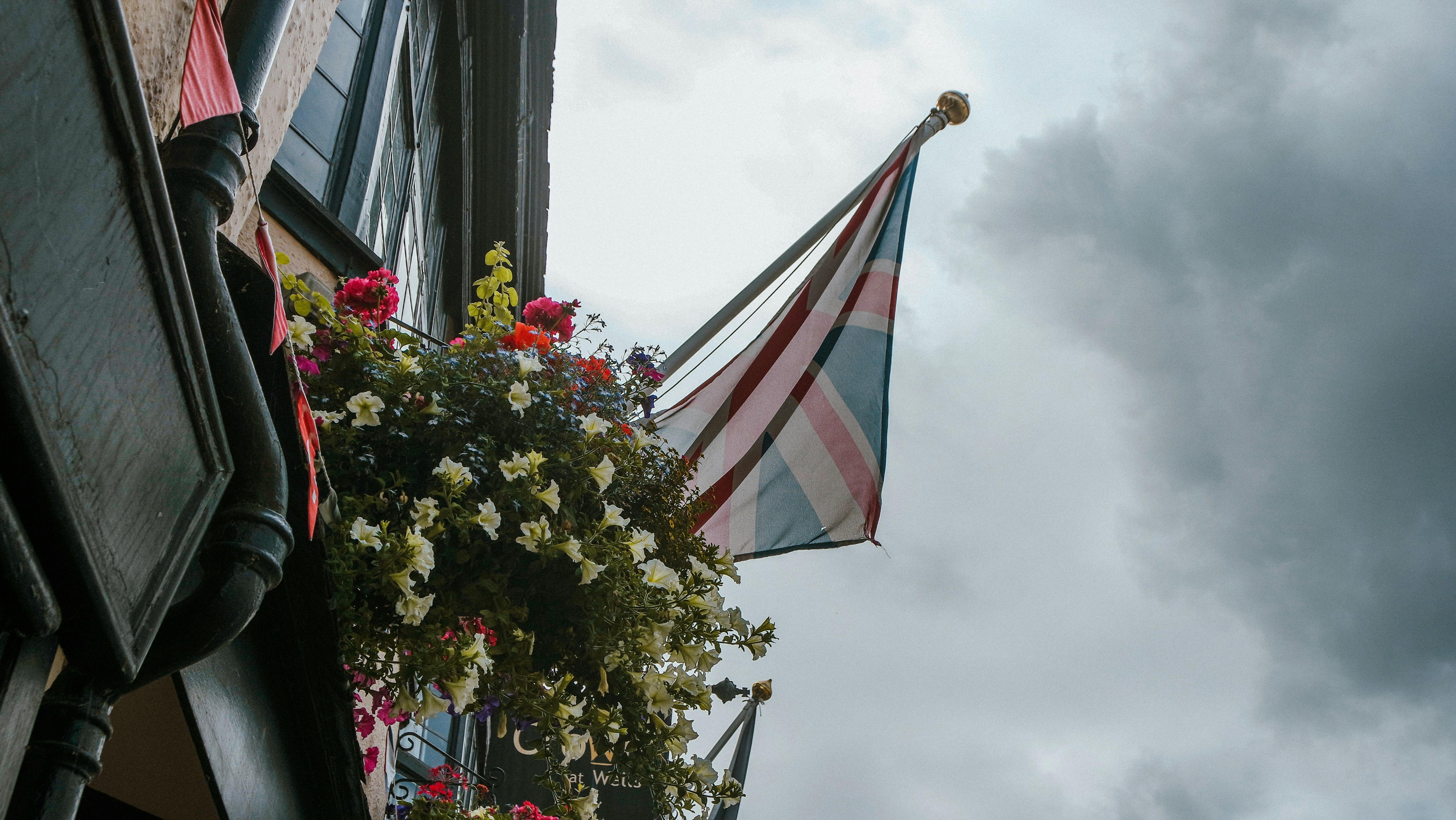 Union Jack flag beside vibrant hanging flowers on a cloudy day.