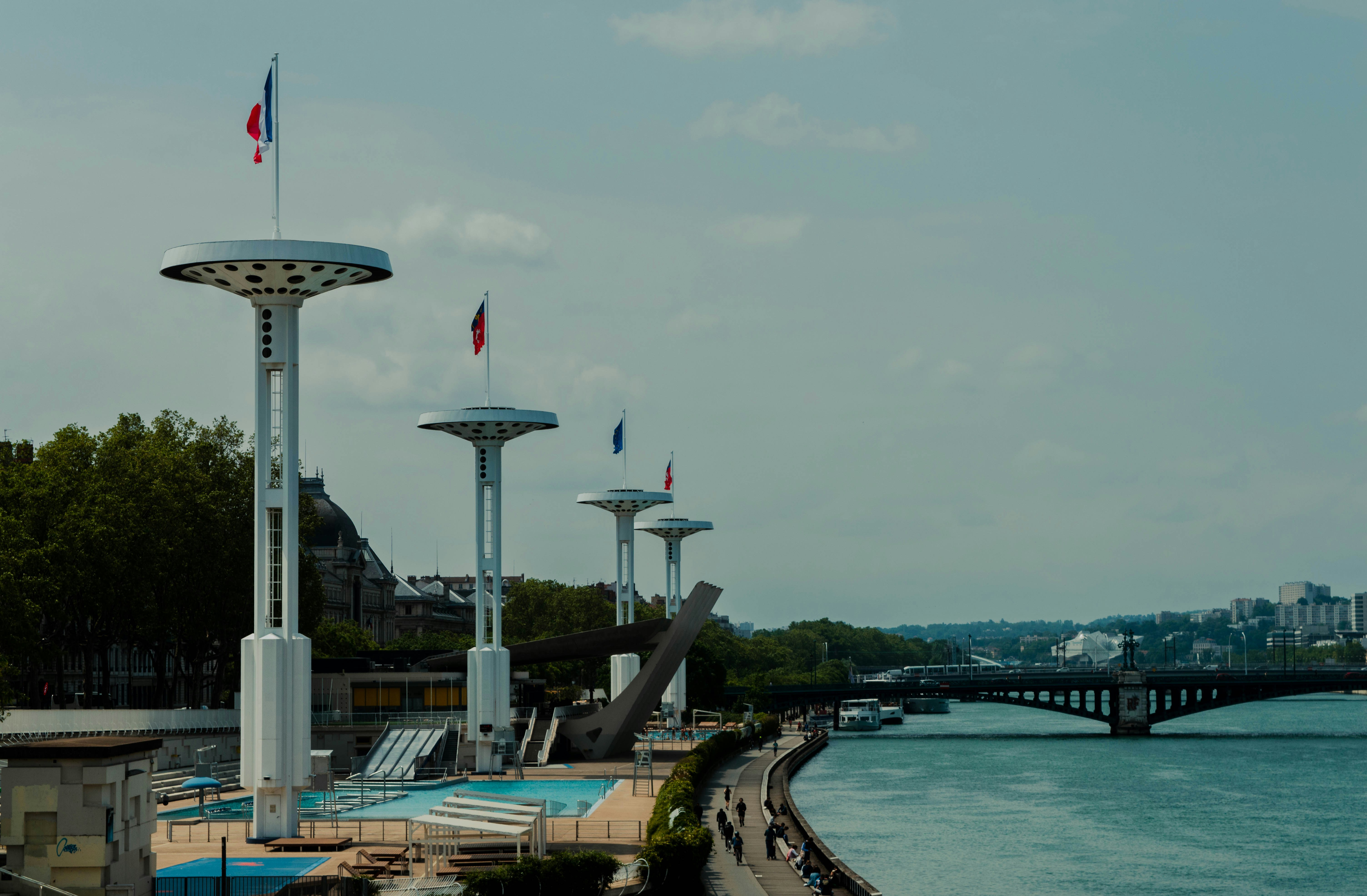 Flag-Topped Pylons Framing a Quiet Riverside Promenade