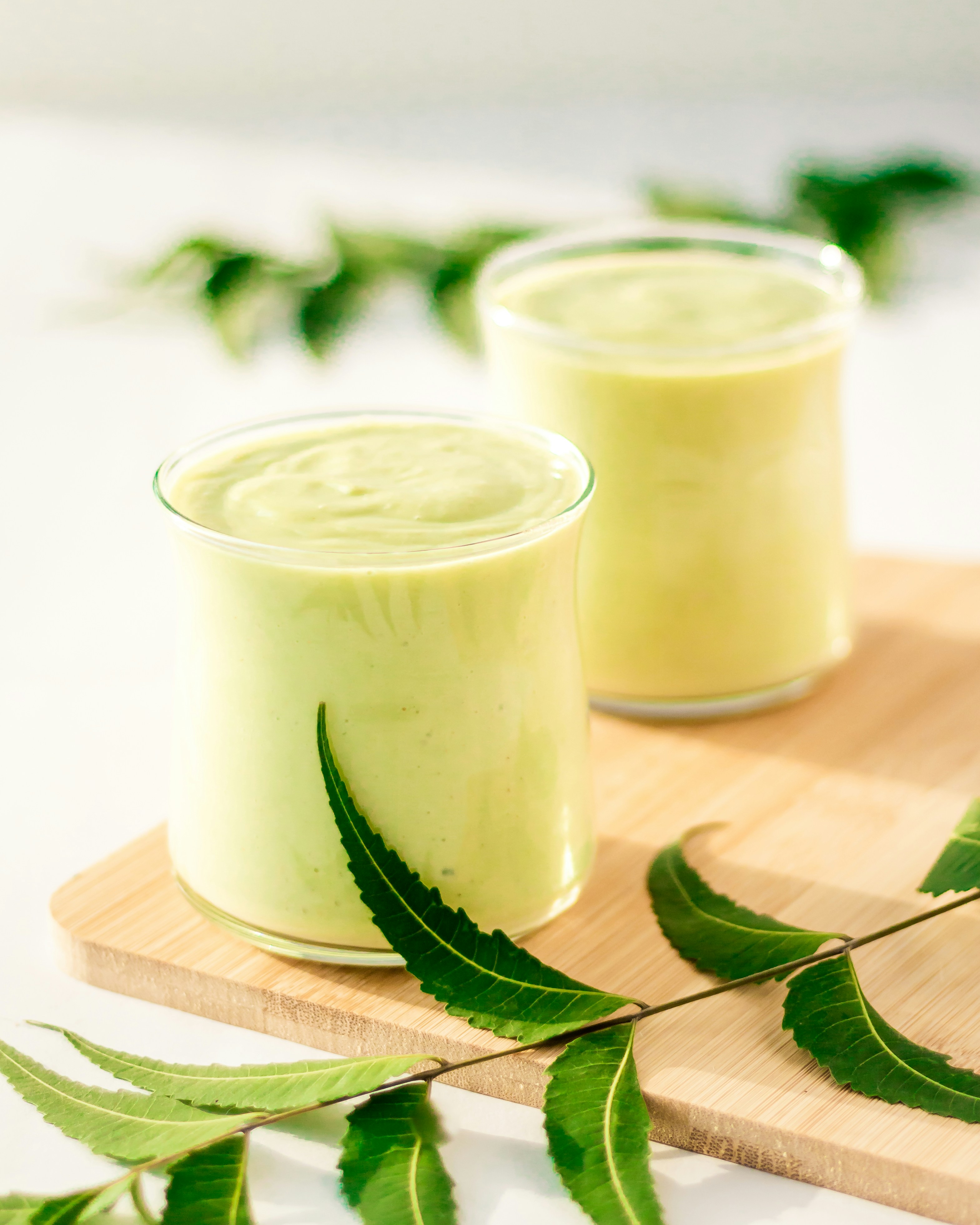 Two Creamy Green Smoothies Framed on a Wooden Board with Fresh Leaves