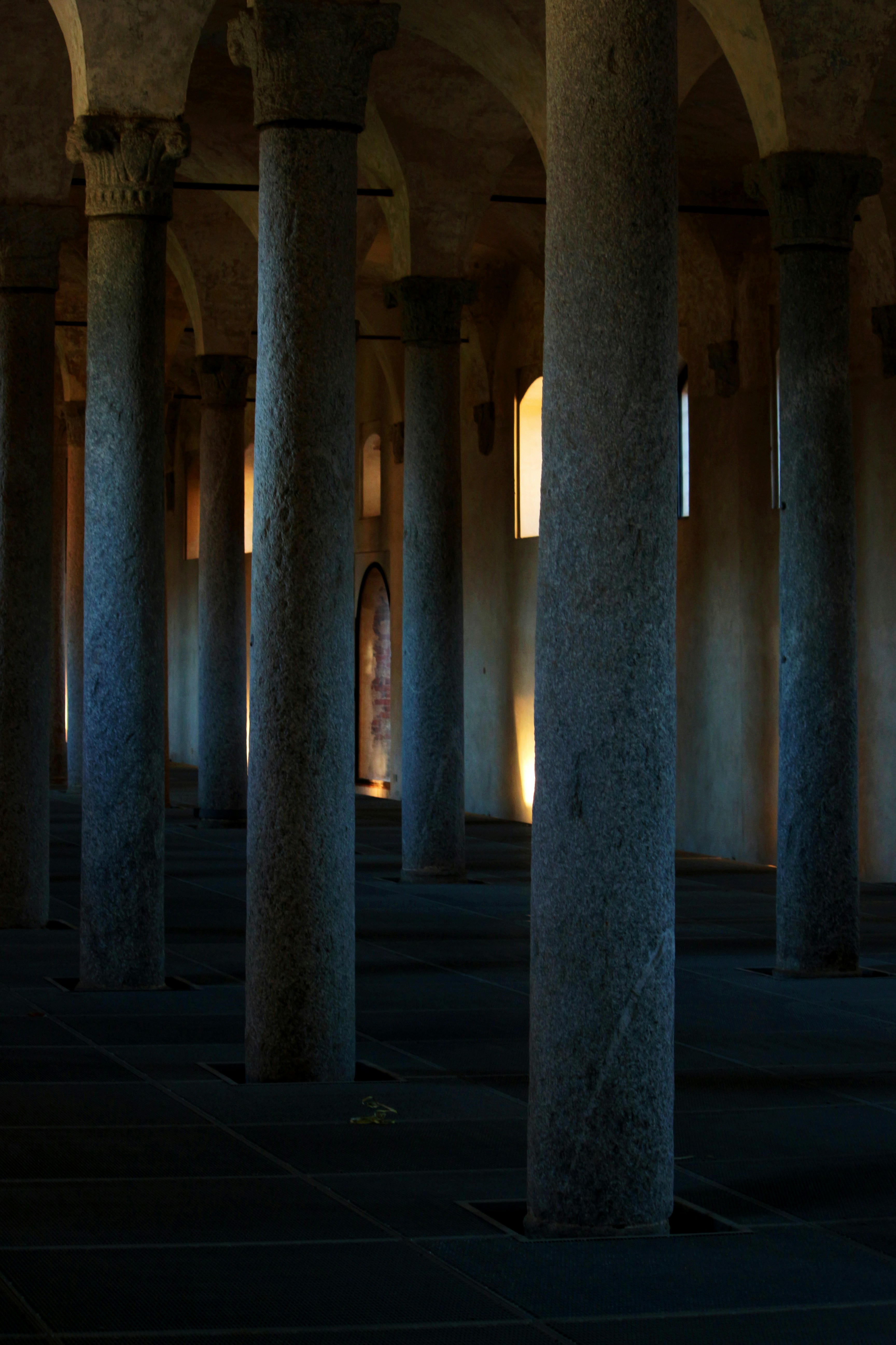 Dimly lit stone columns in a historic architectural interior with soft light filtering through narrow windows.
