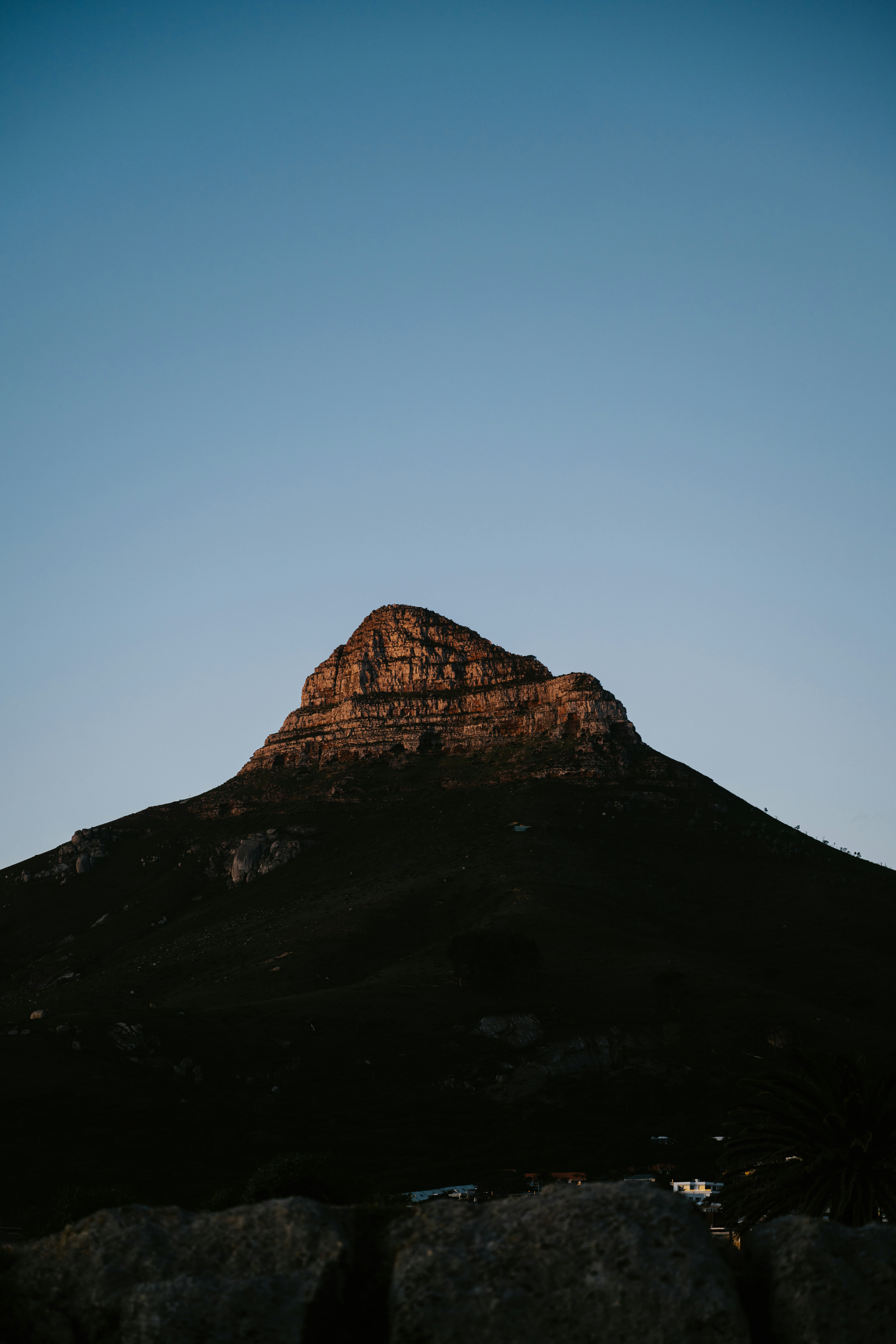 Photograph of a solitary peak rising from shadowed slopes beneath a clear blue sky.