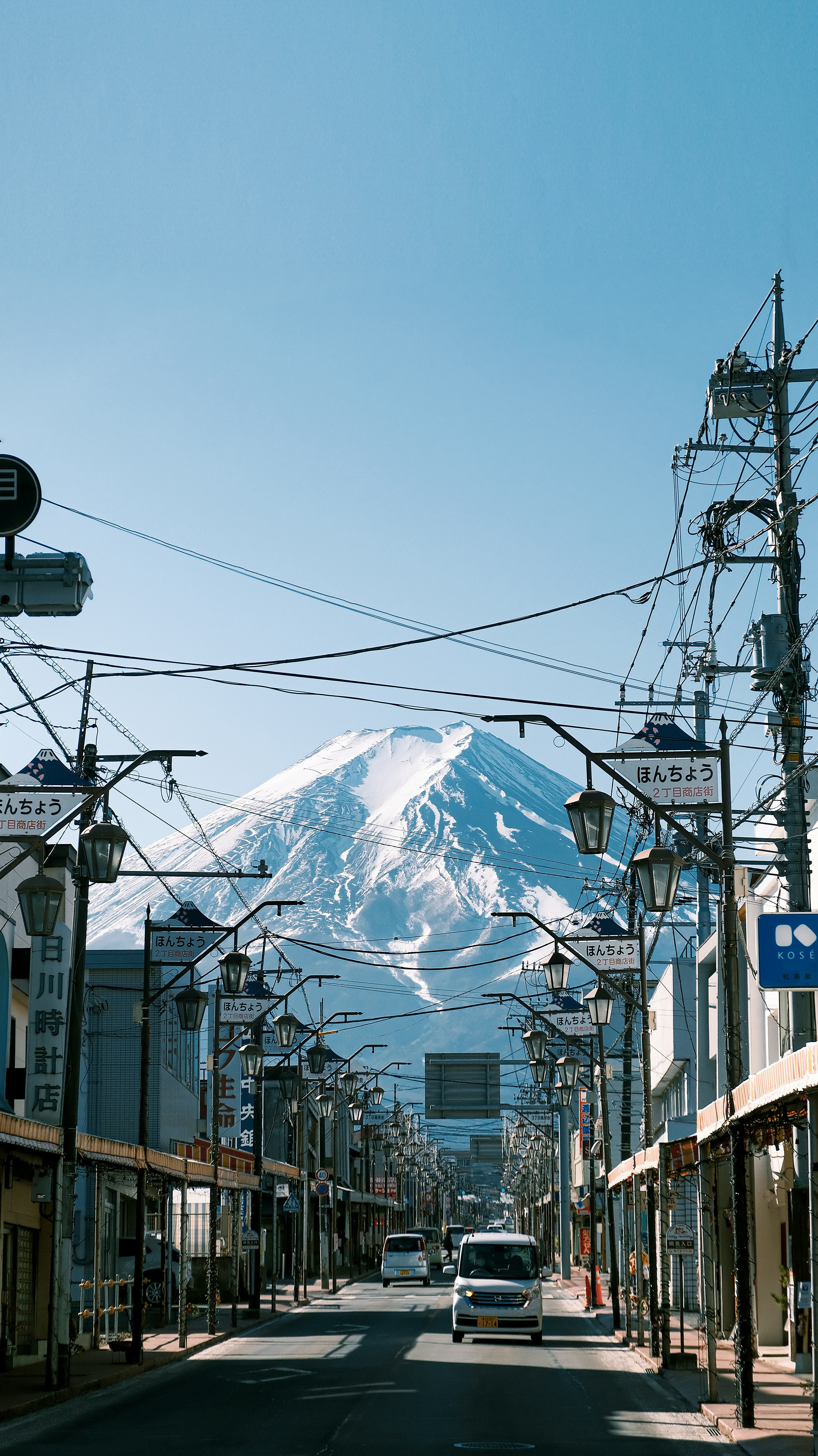 Honcho Street and the Majestic Mt. Fuji_A Captivating Wallpaper of Japan's Stunning Landscape | a car driving down a street with a mountain in the background