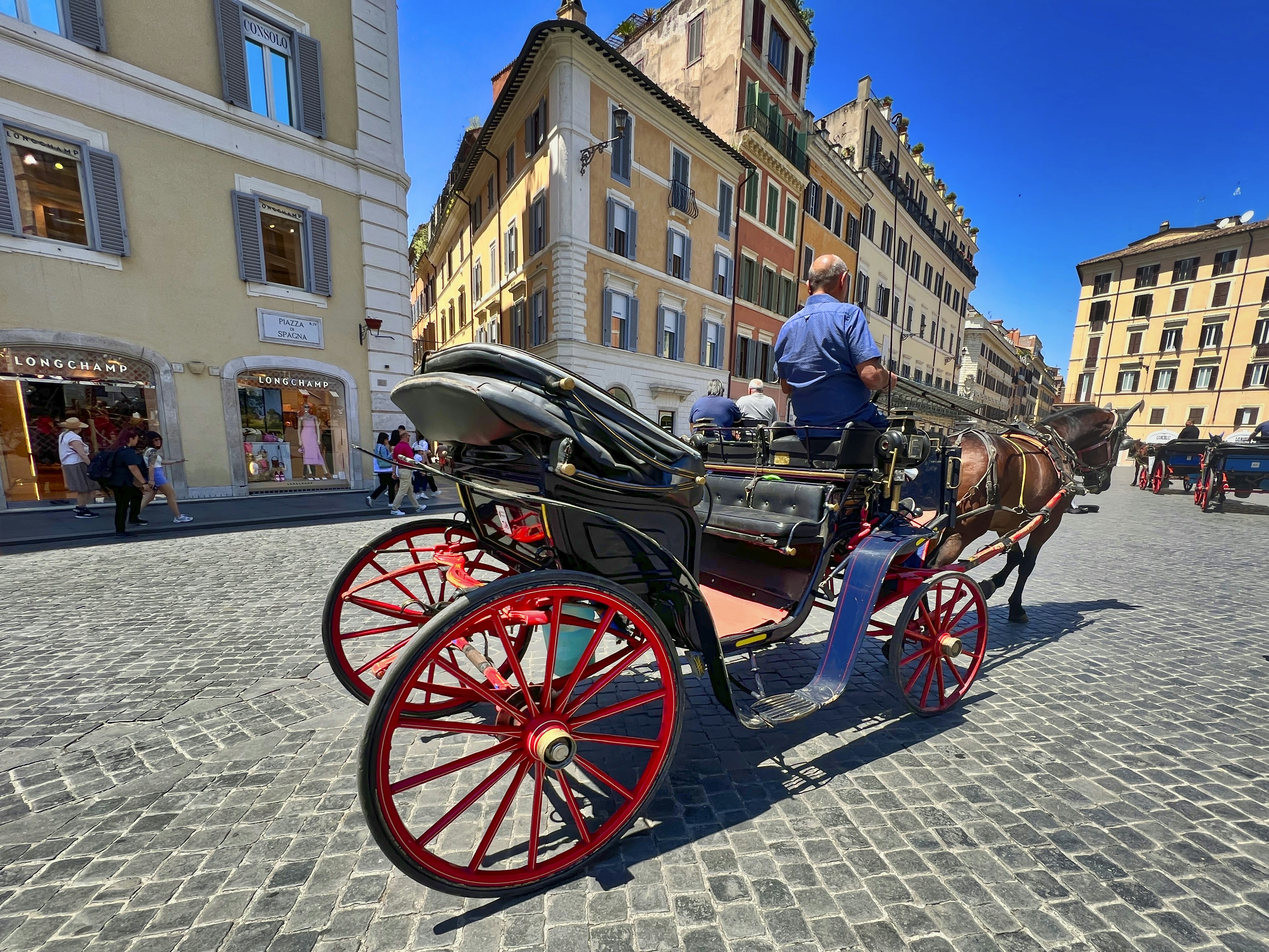 Sunlit Carriage on a European Piazza: Crimson Wheels Under a Clear Sky