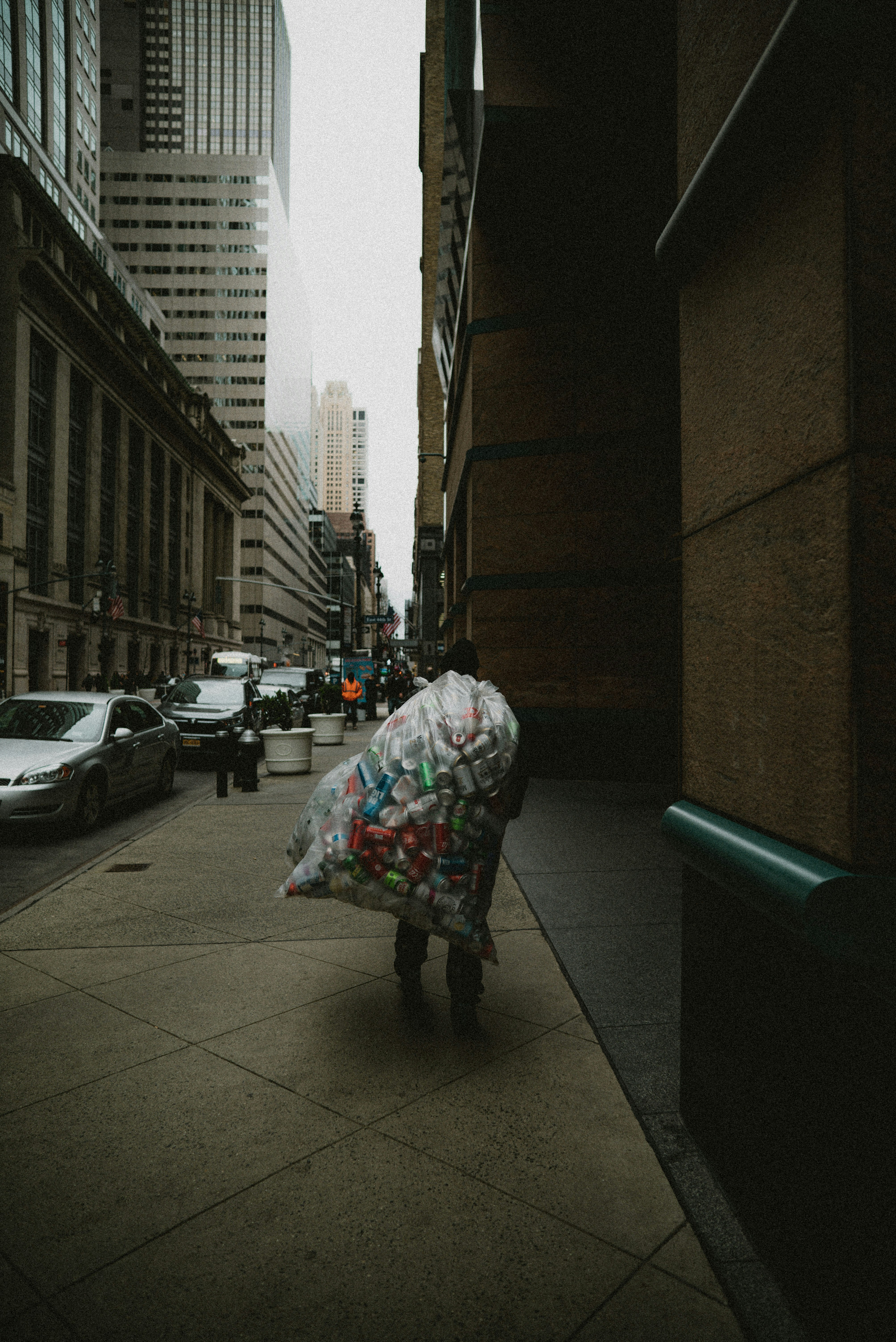 The Bottled Burden: A Lone Recycler Navigates a Concrete Canyon