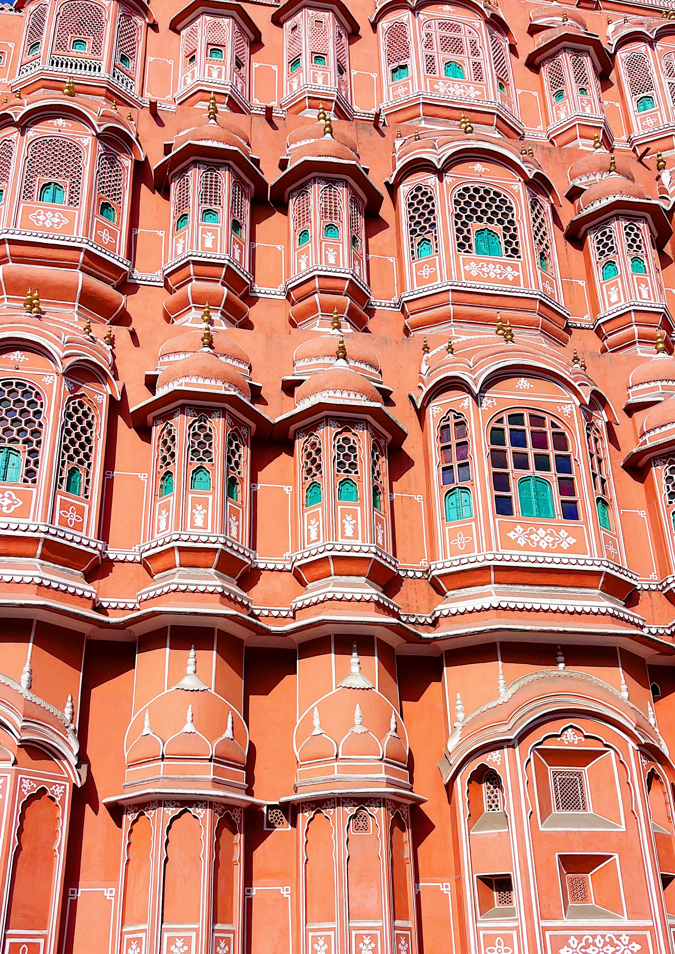 Close-up photograph of the Hawa Mahal's coral-pink facade, featuring layered jharokhas and intricate latticework.