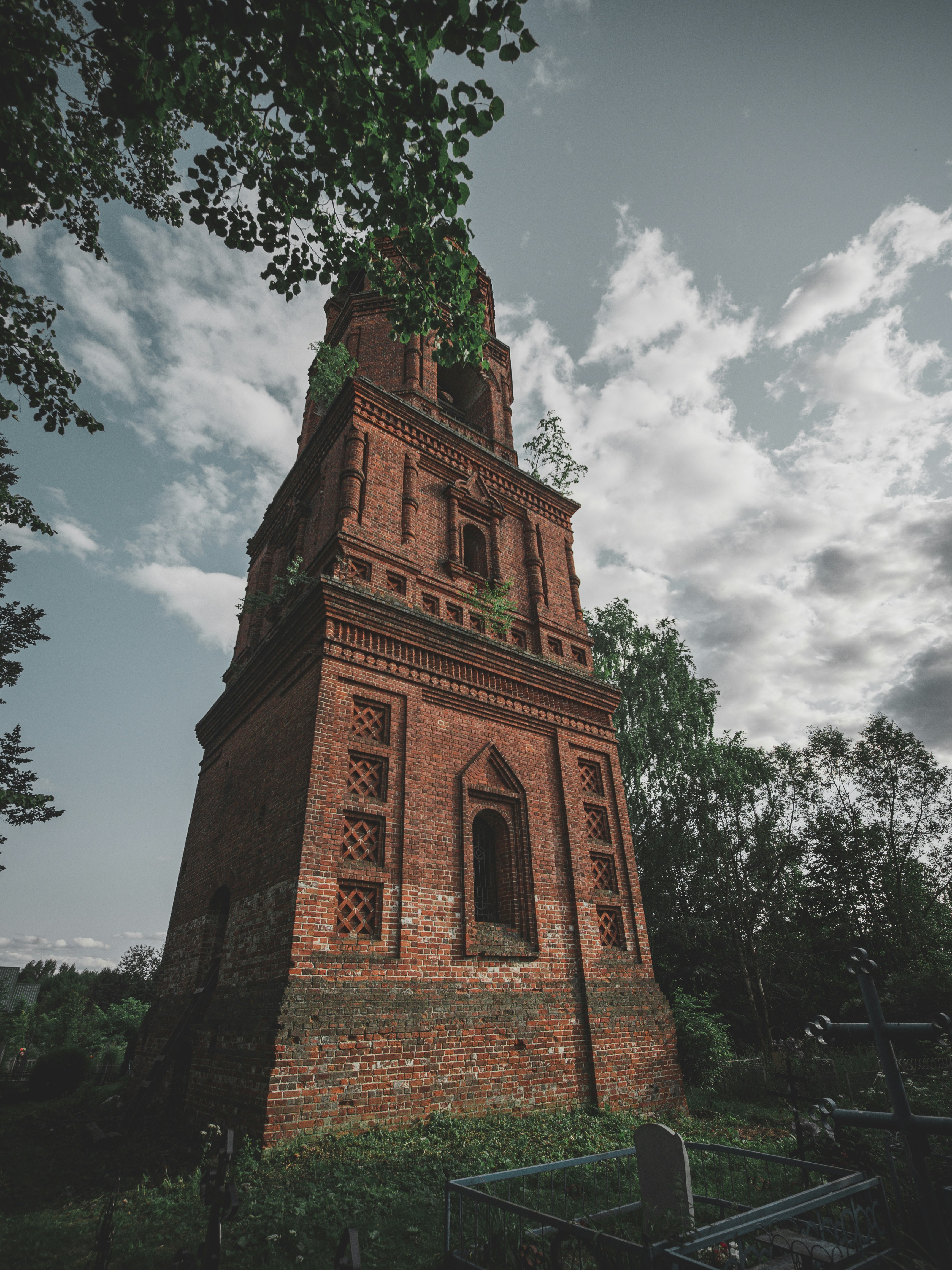Brick Tower Rising Through a Green Canopy Under a Cloudy Sky