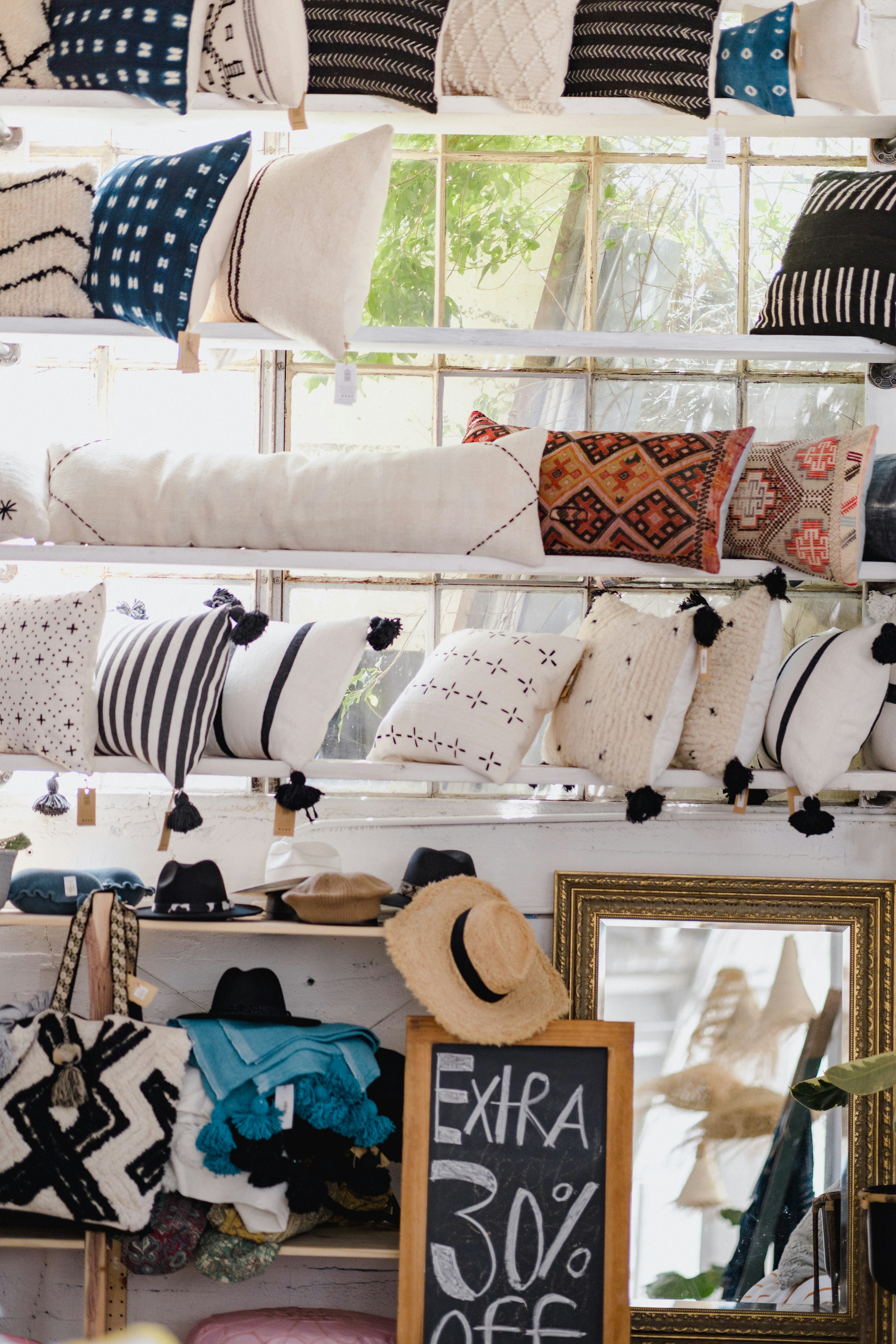 Sunlit Pillow Parade: Cushions, Hats, and a Chalkboard Sale in a Cozy Boutique
