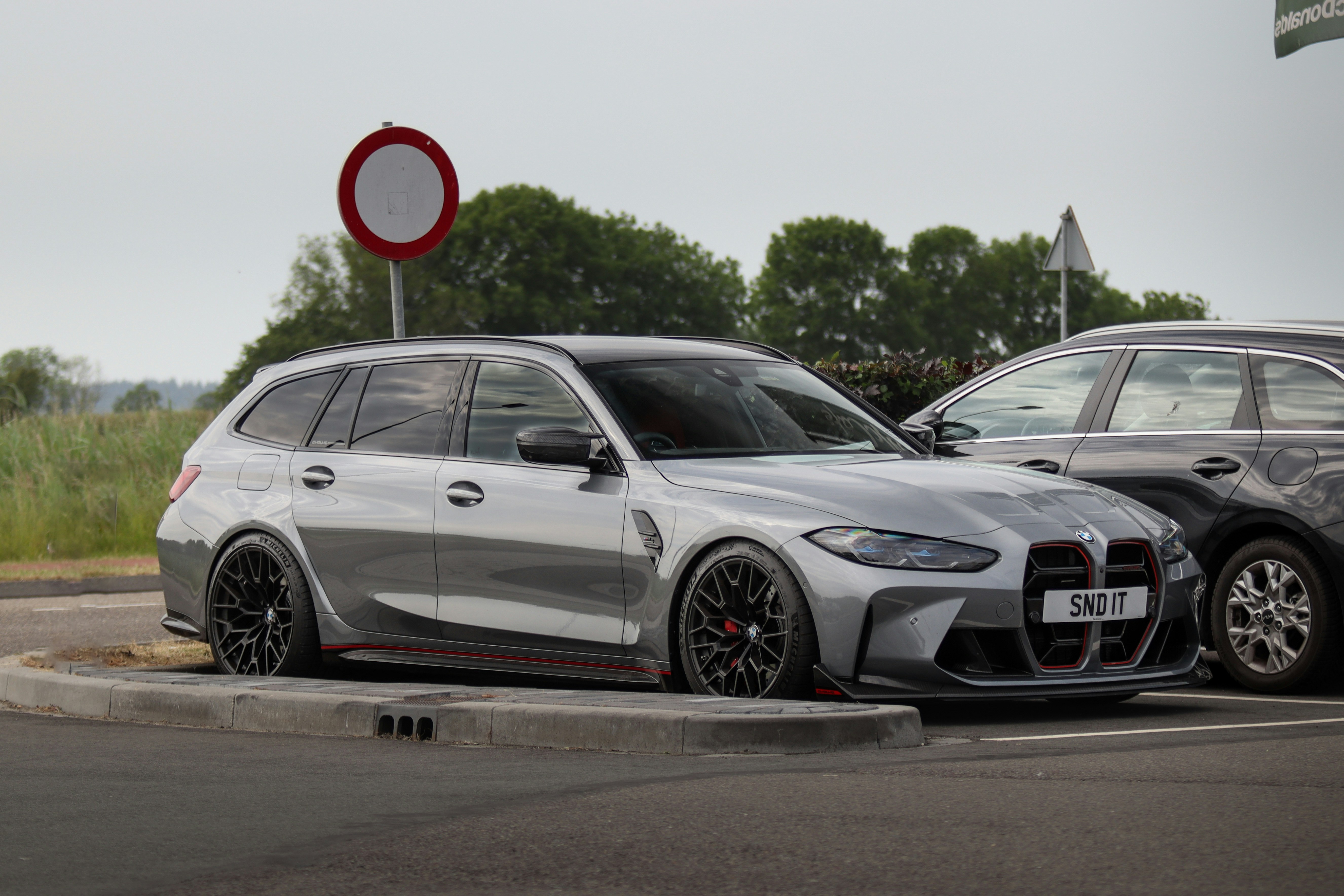 Curbside Velocity: A silver sport-wagon with wide wheels anchors a car meet