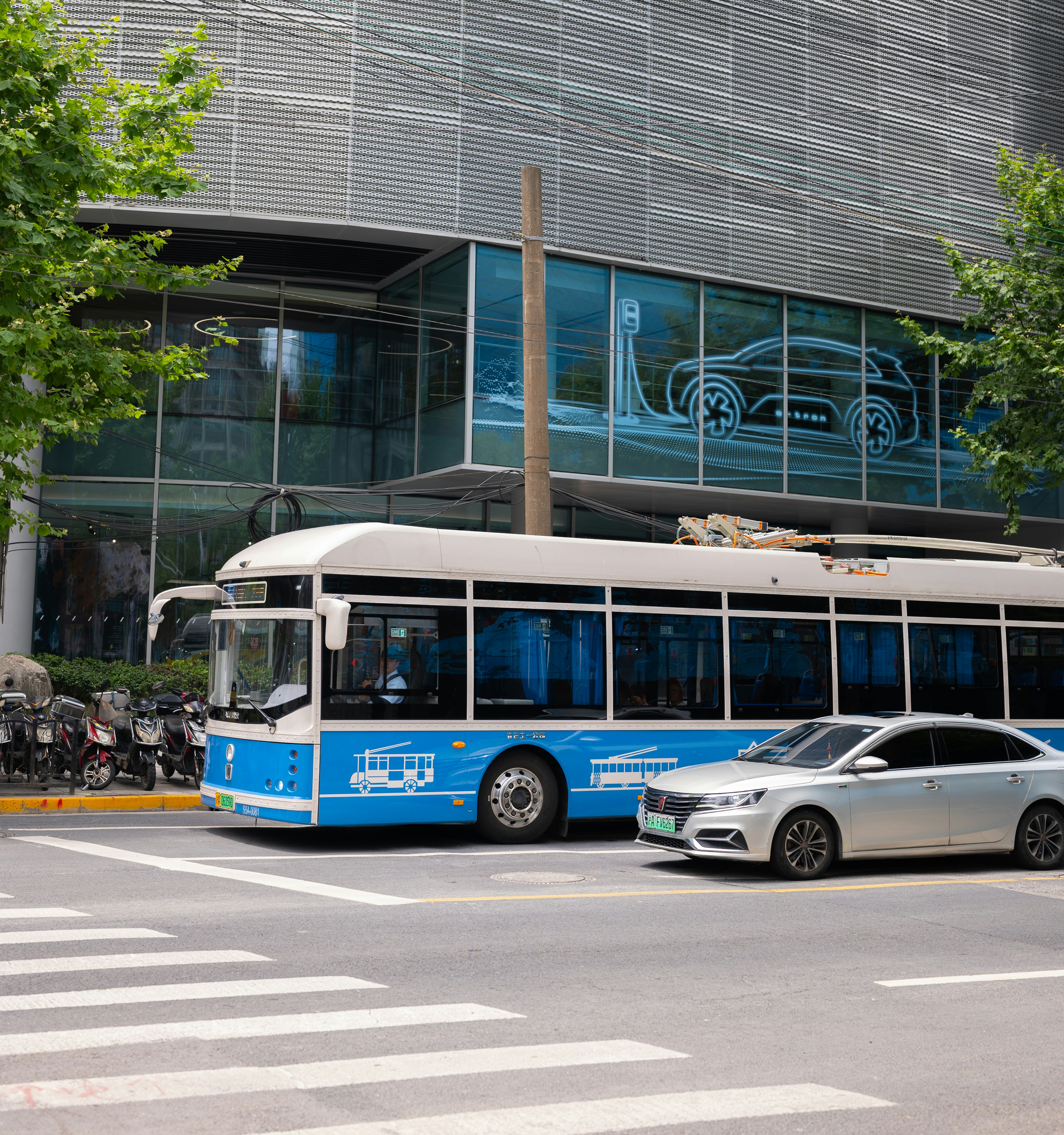 Blue City Bus Framed by Modern Glass Facade and a Car Mural