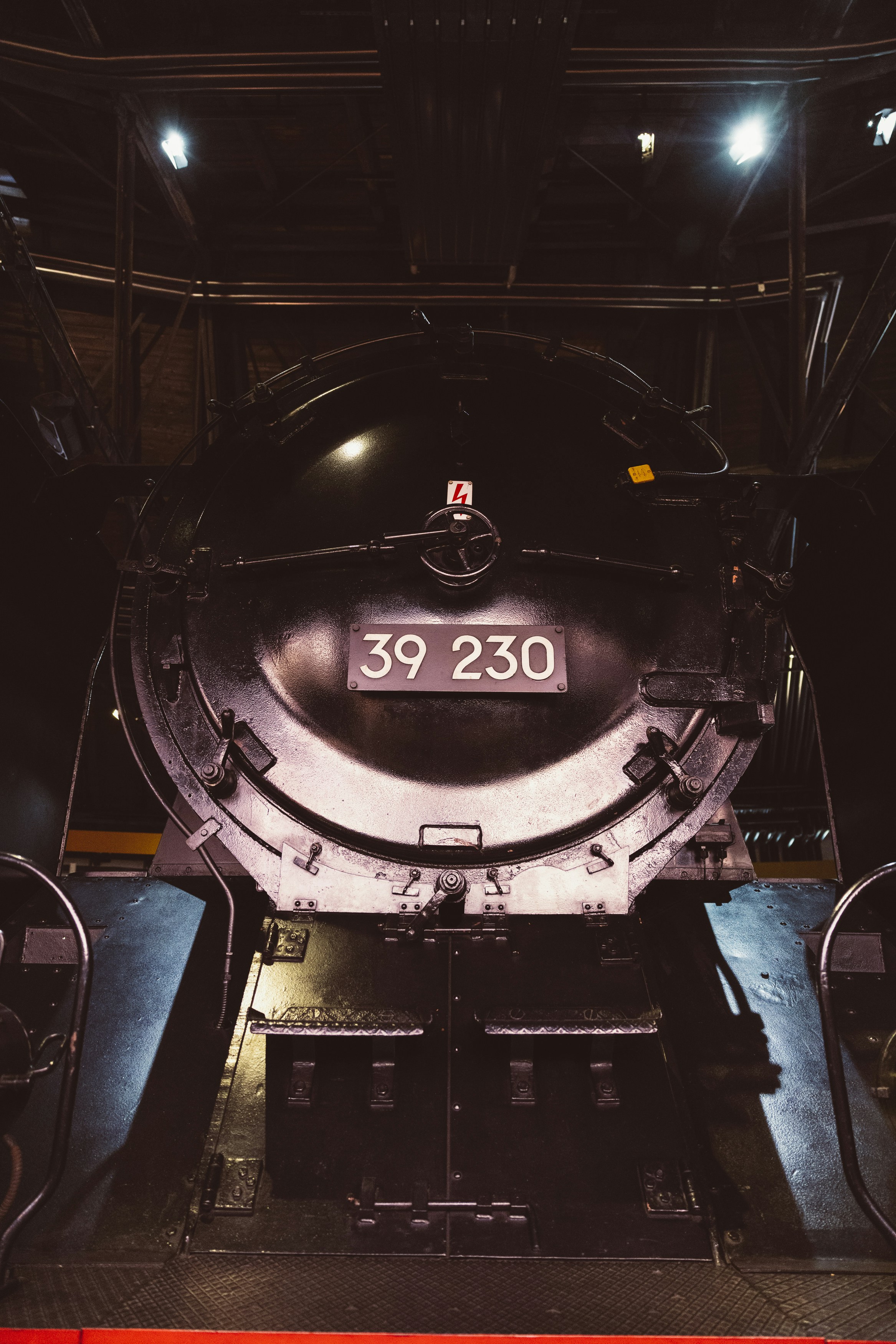Close-up of a vintage steam locomotive's boiler, showcasing its intricate details and the number 39 230 prominently displayed. The industrial setting highlights the machine's robust design.