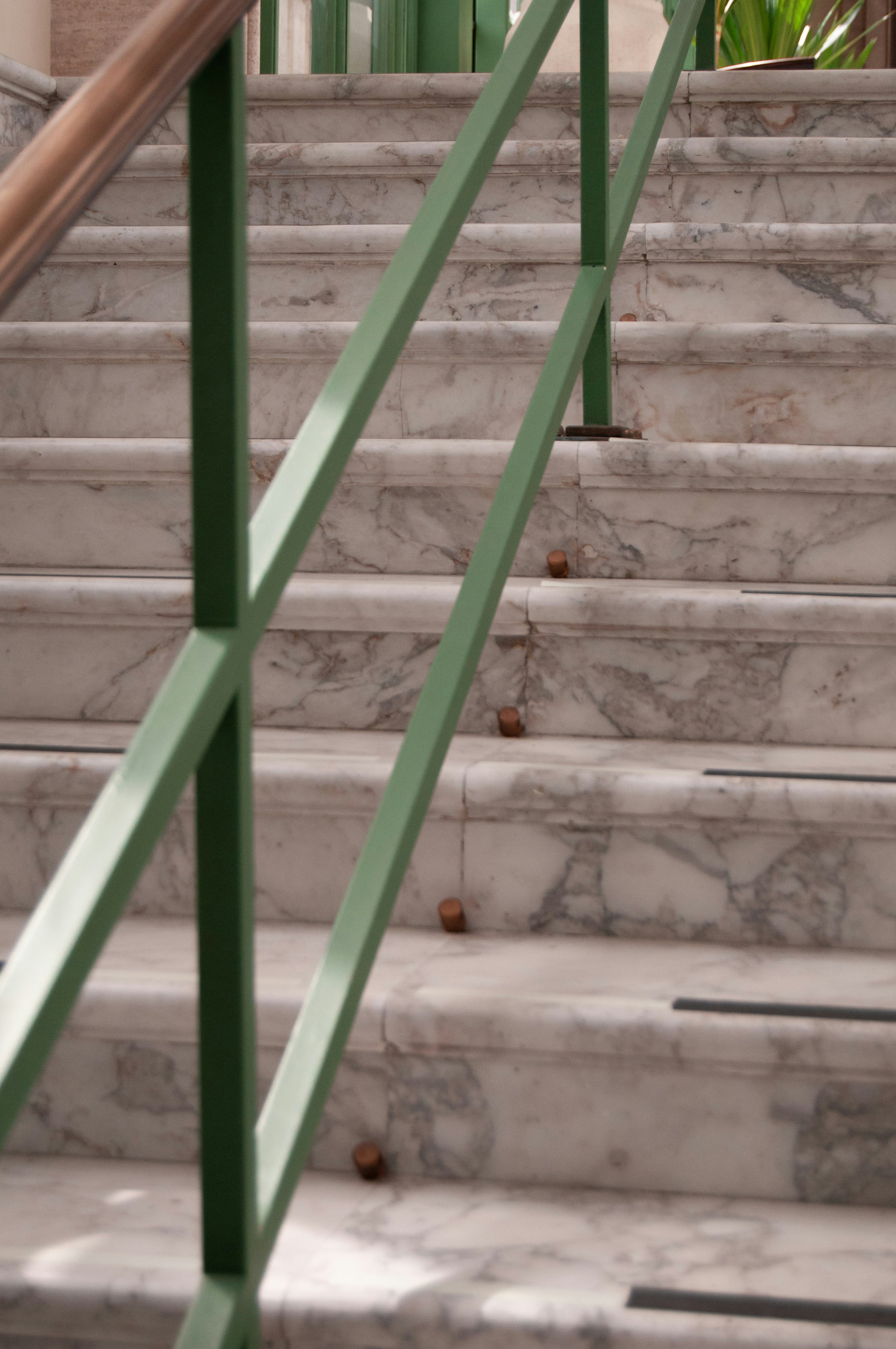Marble staircase adorned with green railings, leading upward in a well-lit space. The smooth texture of the steps contrasts with the vibrant railing.
