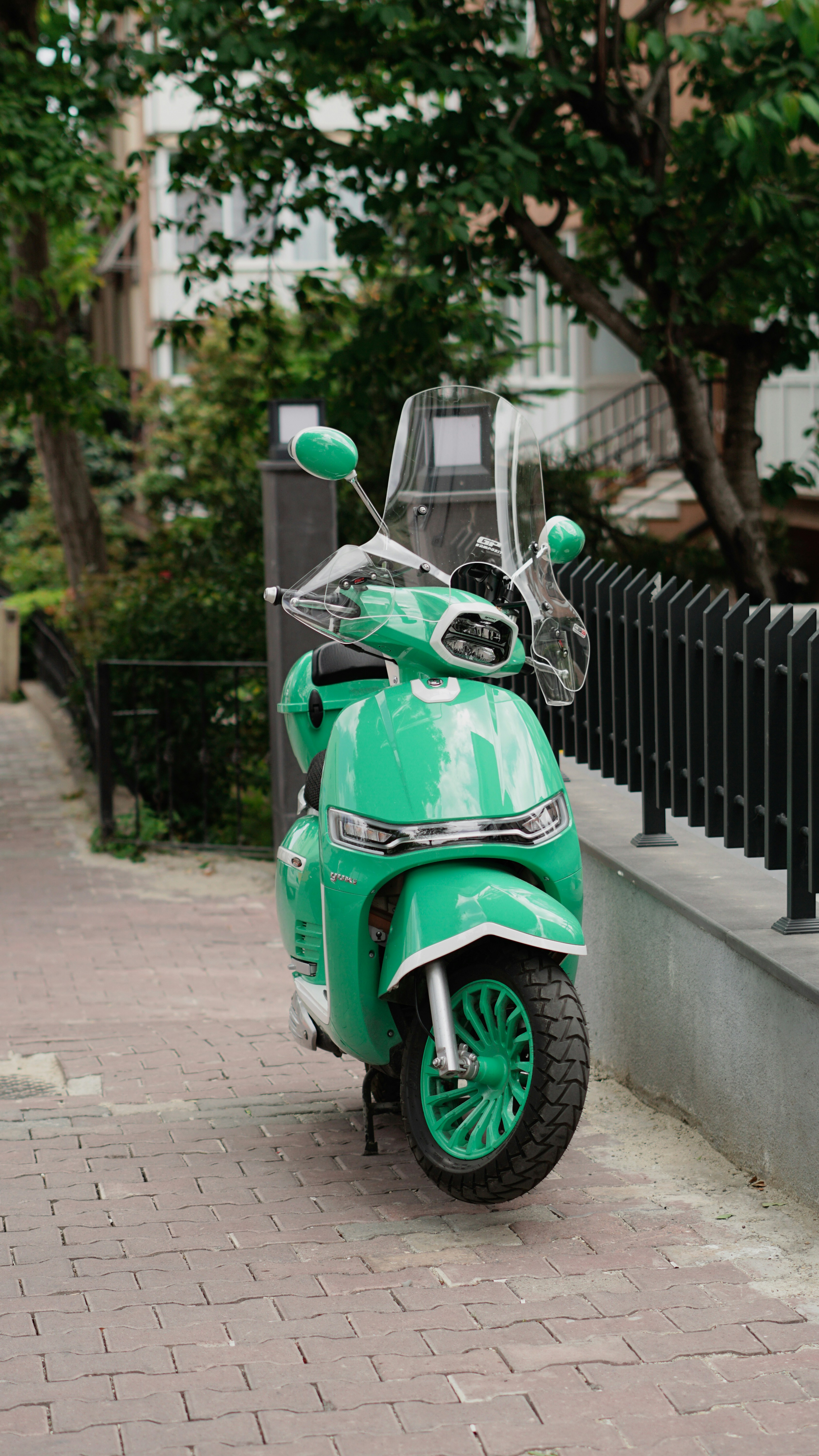 Emerald Scooter Guarded by City Railings and Green Canopy