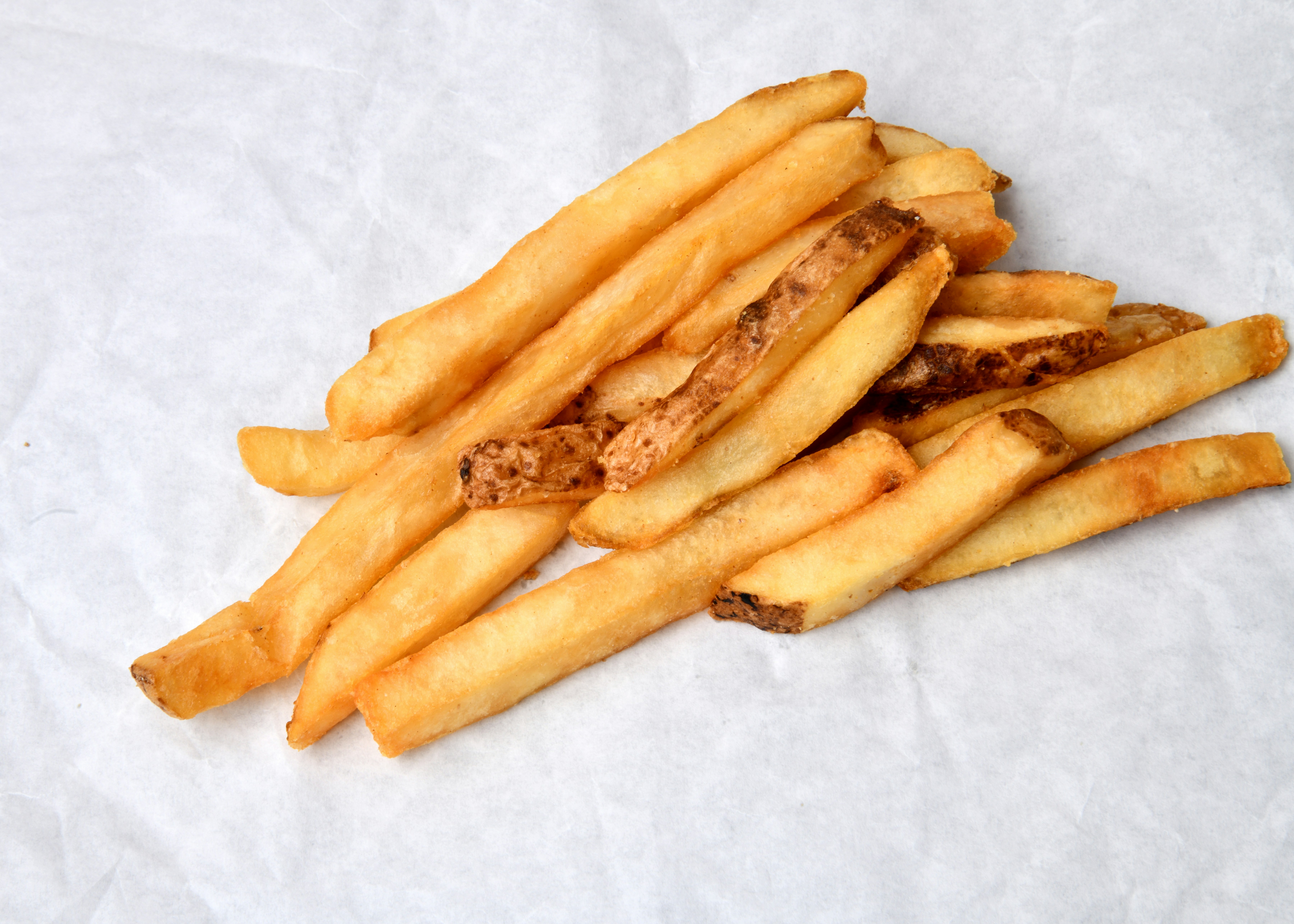 Crispy golden French fries arranged haphazardly on a light background.