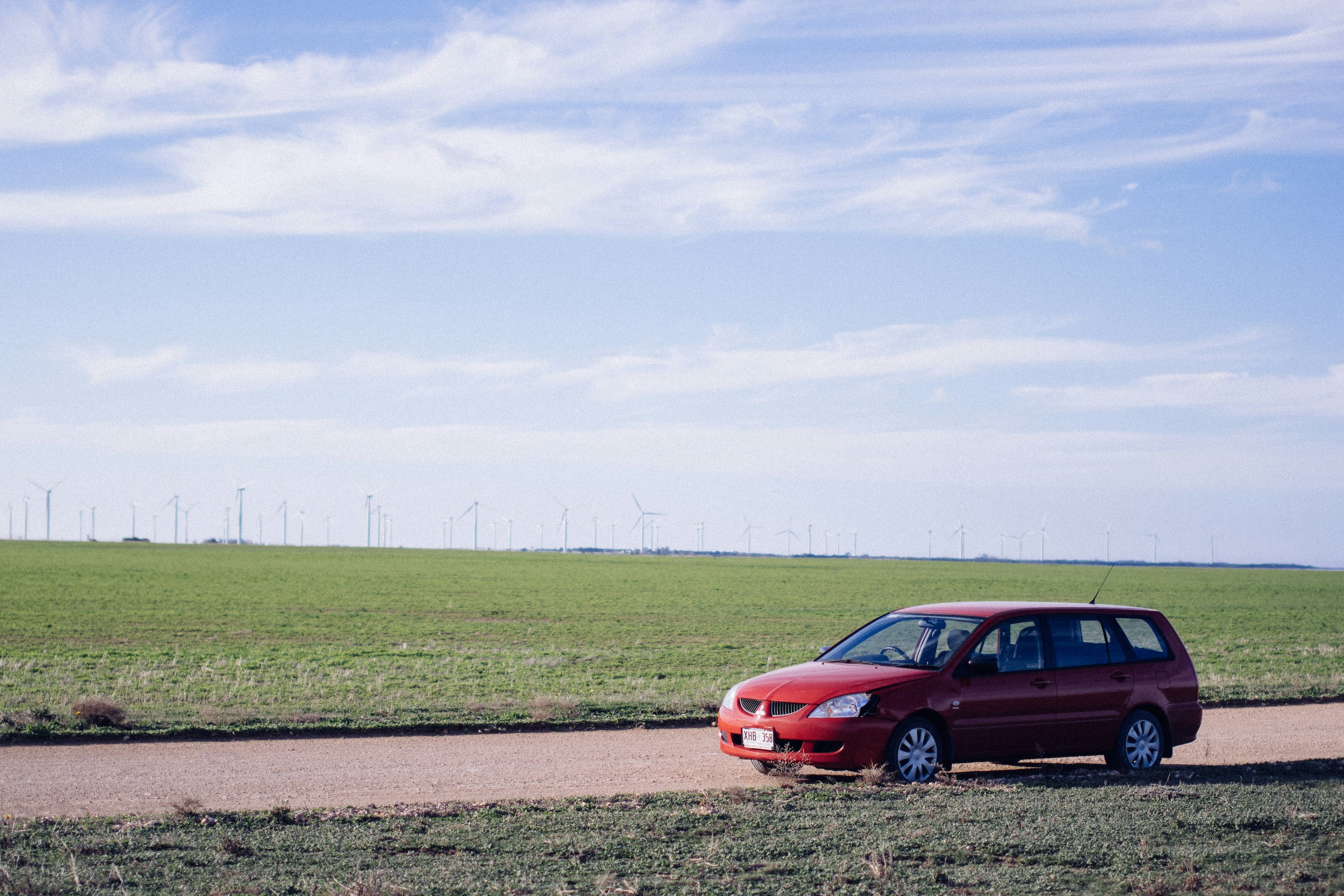 Red Station Wagon on a Quiet Road Beneath a Field of Wind Turbines