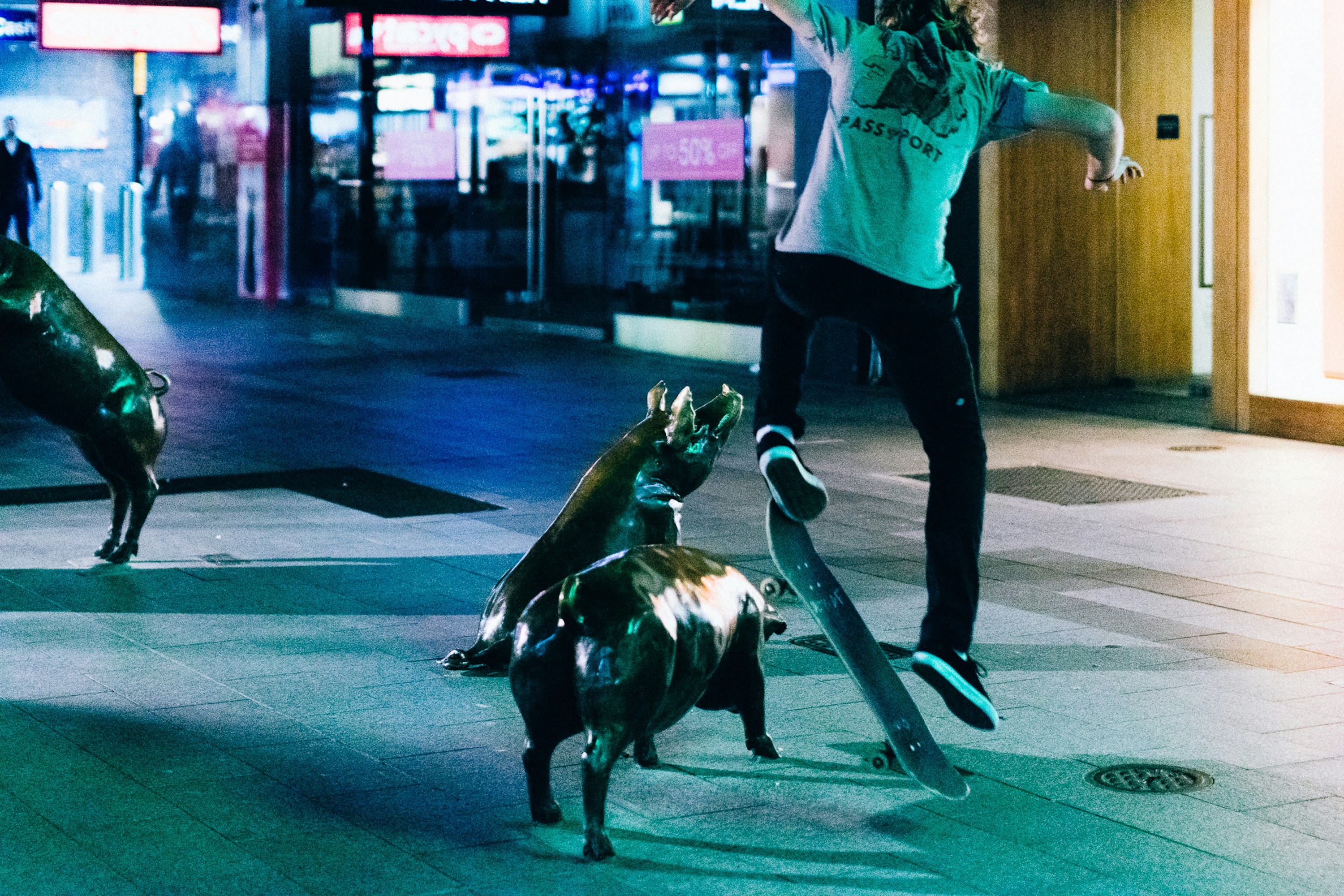 Midair on Neon Streets: Skater Jumps Past a Polished Dog Sculpture