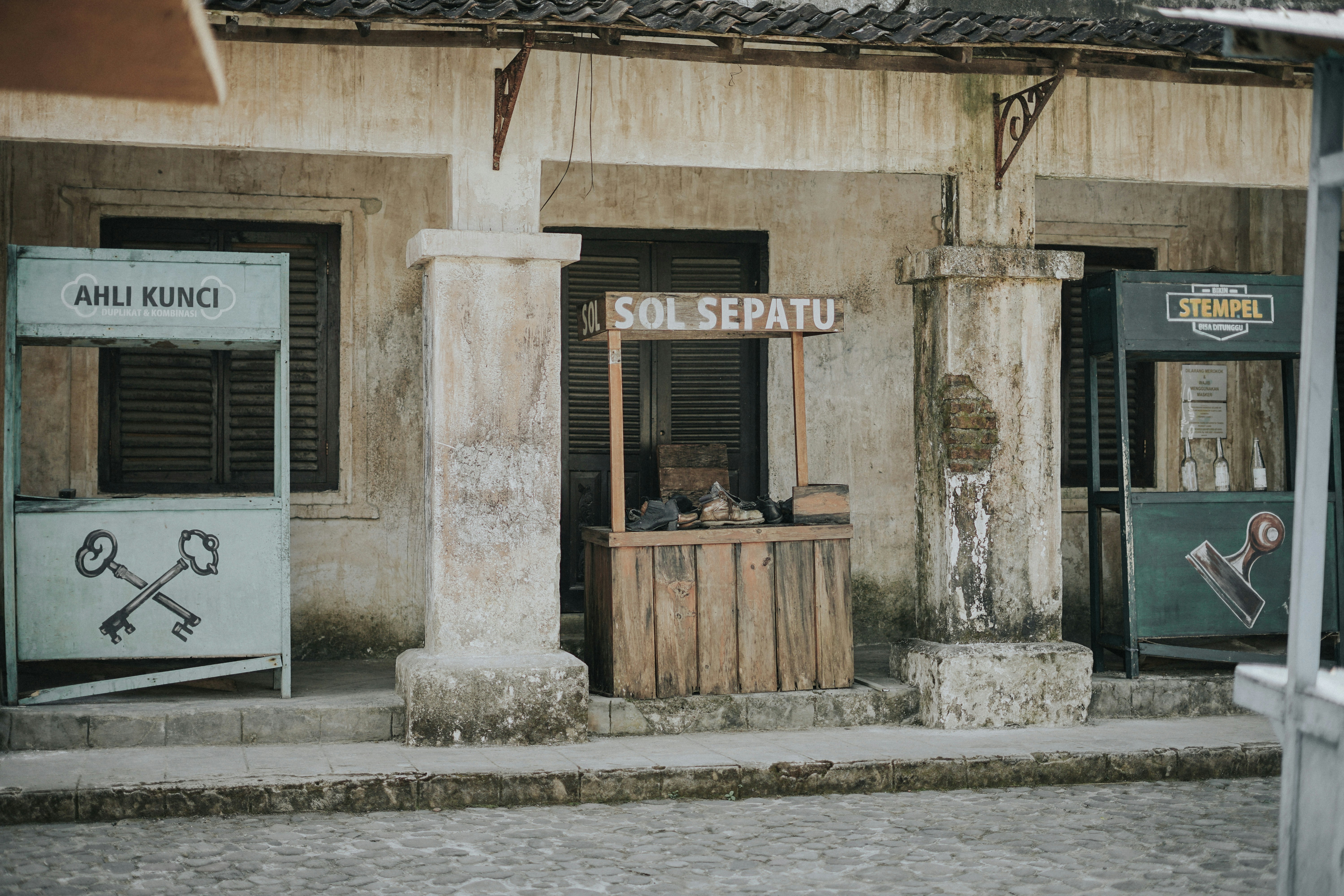Weathered Arcade Front: SOL SEPATU and AHLI KUNCI Along a Cobblestone Street
