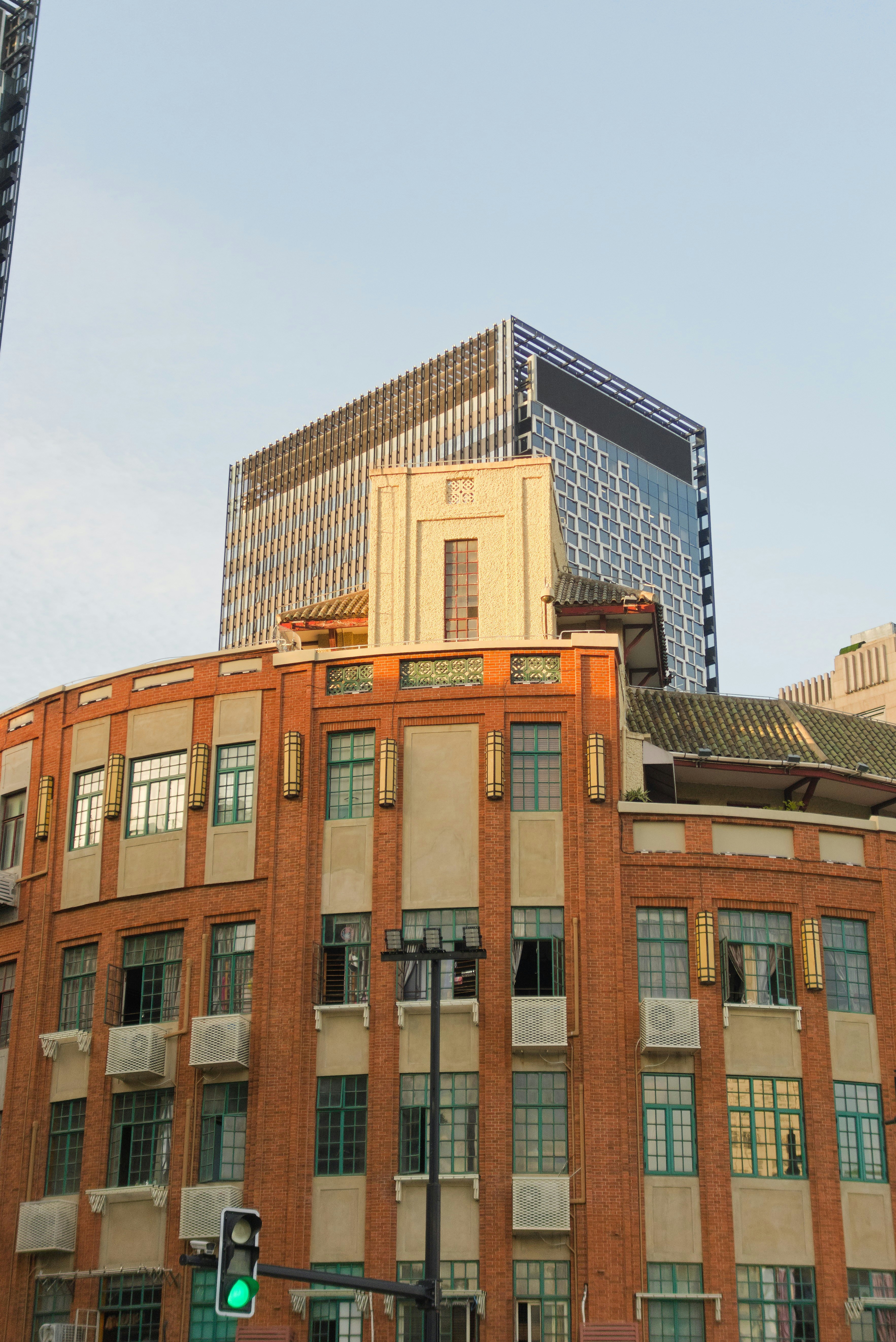 A historic building with red brick and green windows juxtaposed against a modern skyscraper, showcasing architectural evolution. The scene captures urban contrasts under a clear sky.