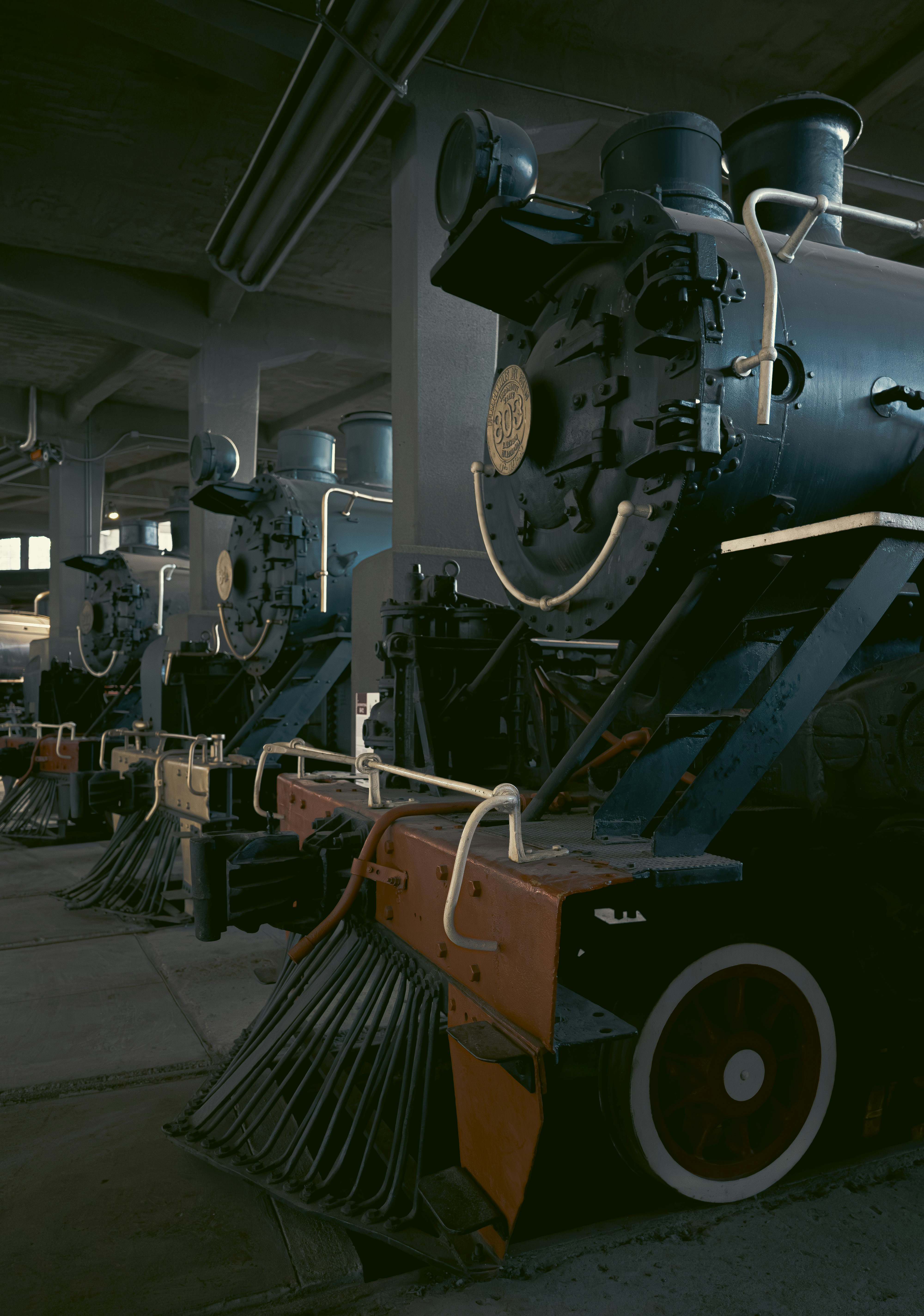 Lead Steam Engine Among Silent Giants in a Dim Depot