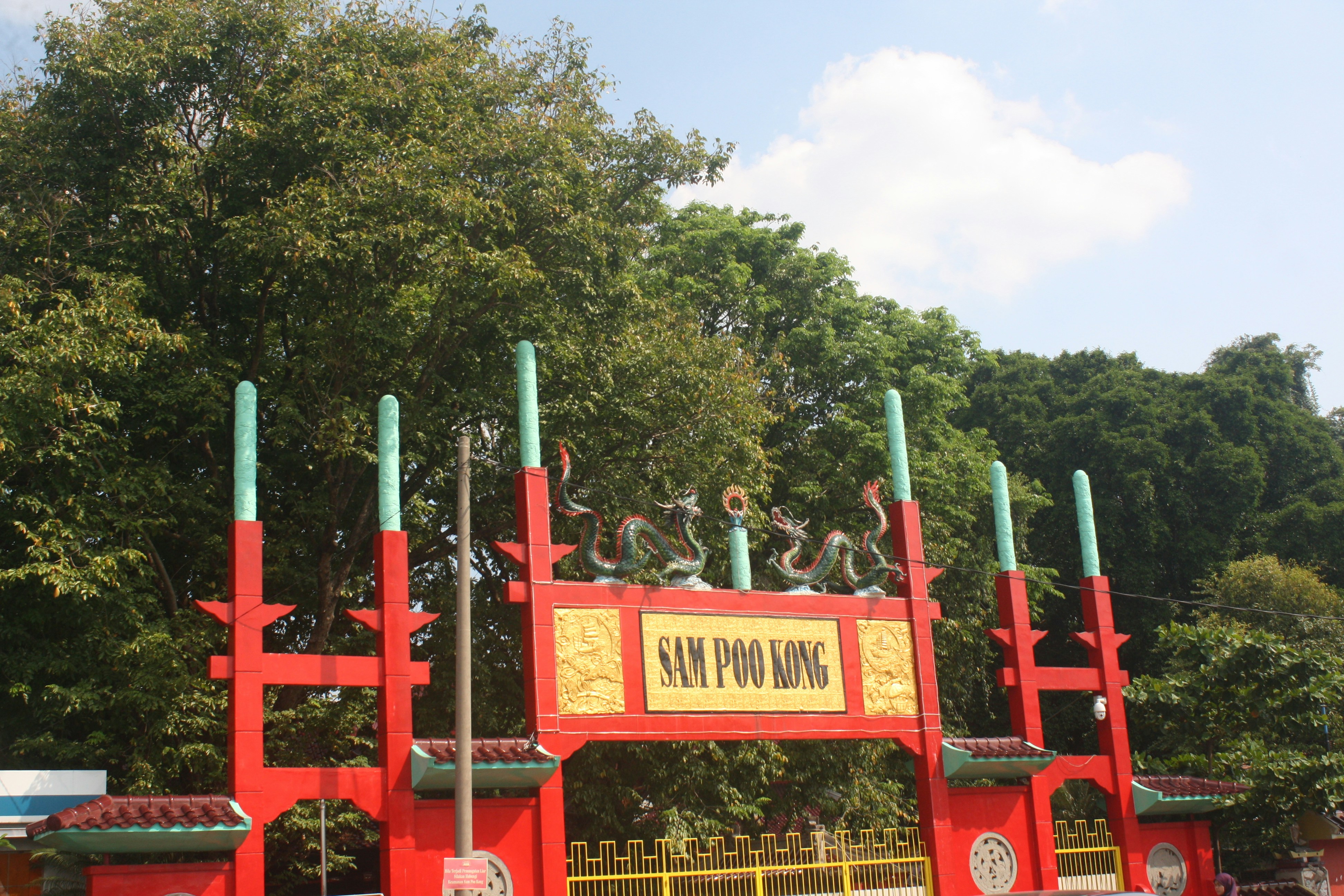 Red and green traditional archway surrounded by lush trees under a clear sky.
