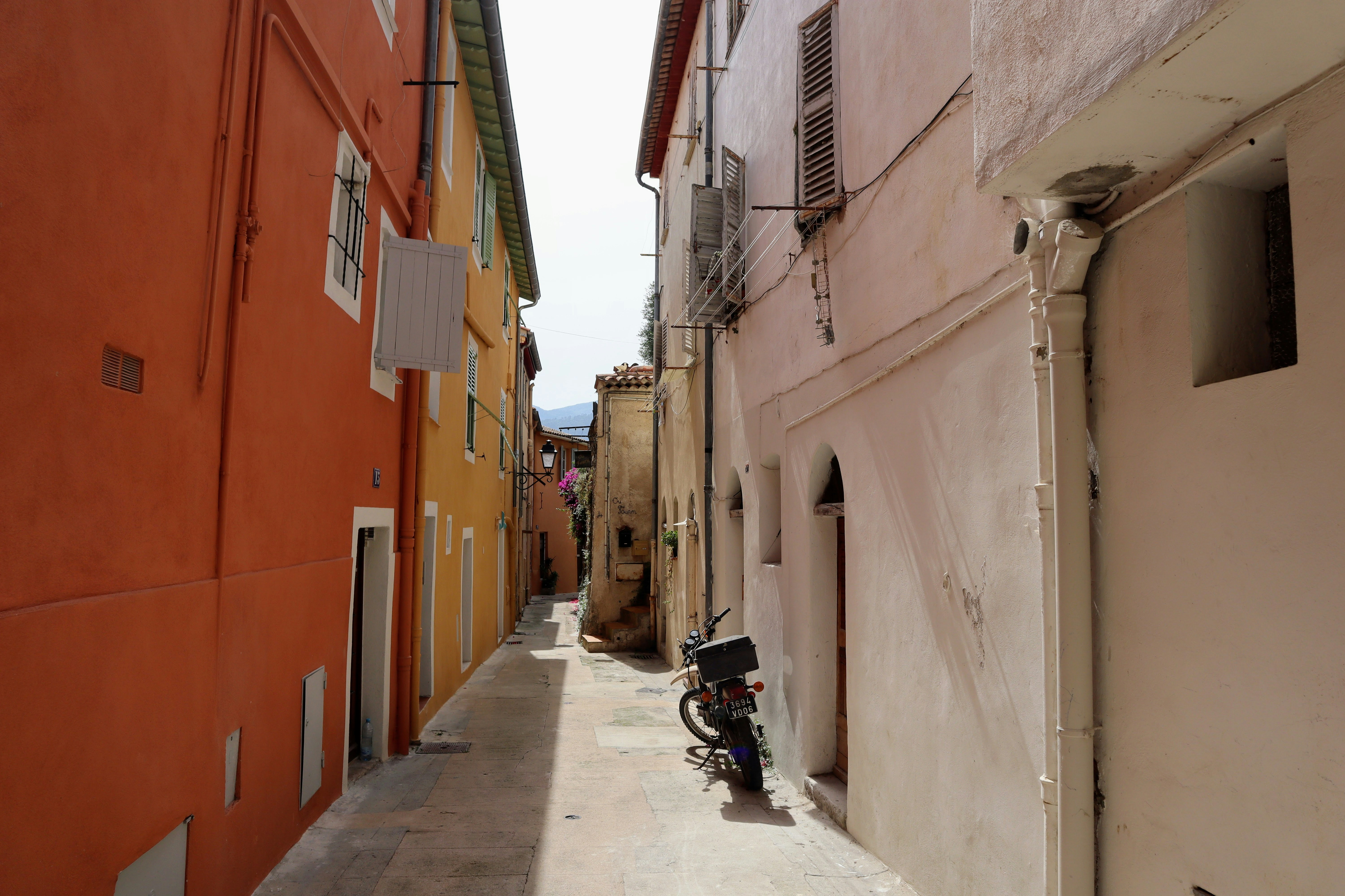 Narrow alley with colorful buildings and a parked scooter under bright daylight.